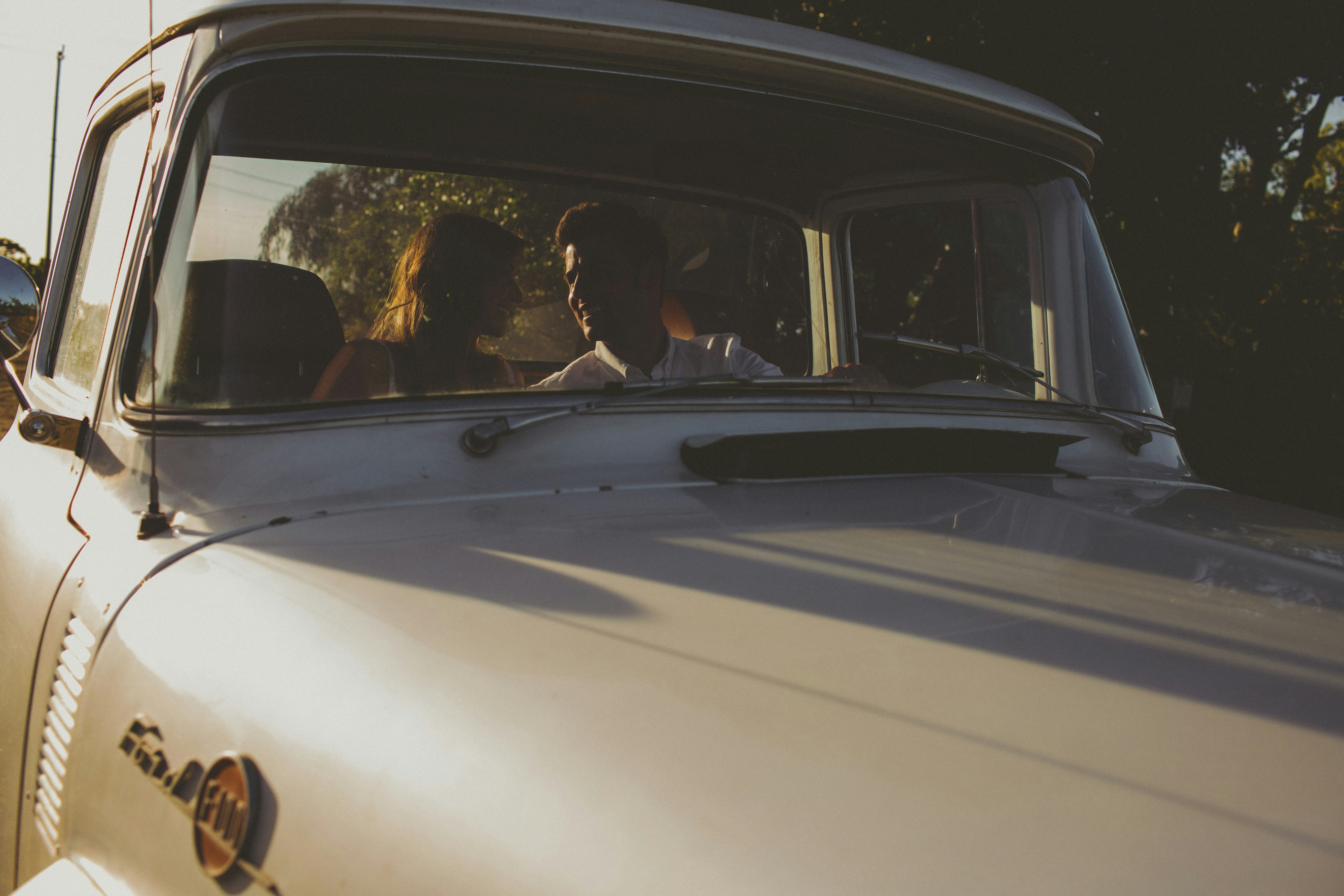 Two people sitting in a vintage car with sunlight casting soft shadows.