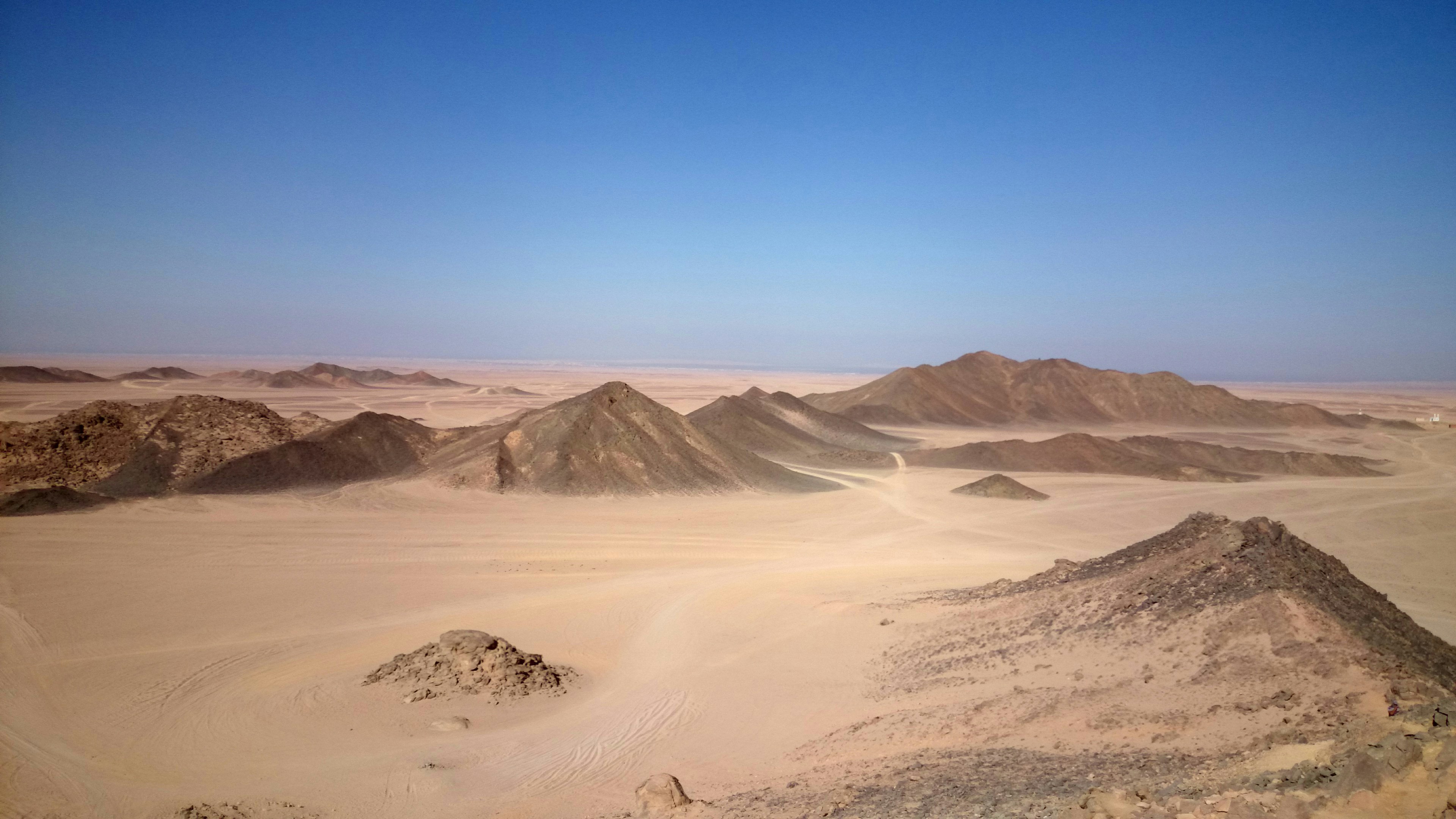 Vast desert landscape with rolling dunes and distant mountains under a clear blue sky.