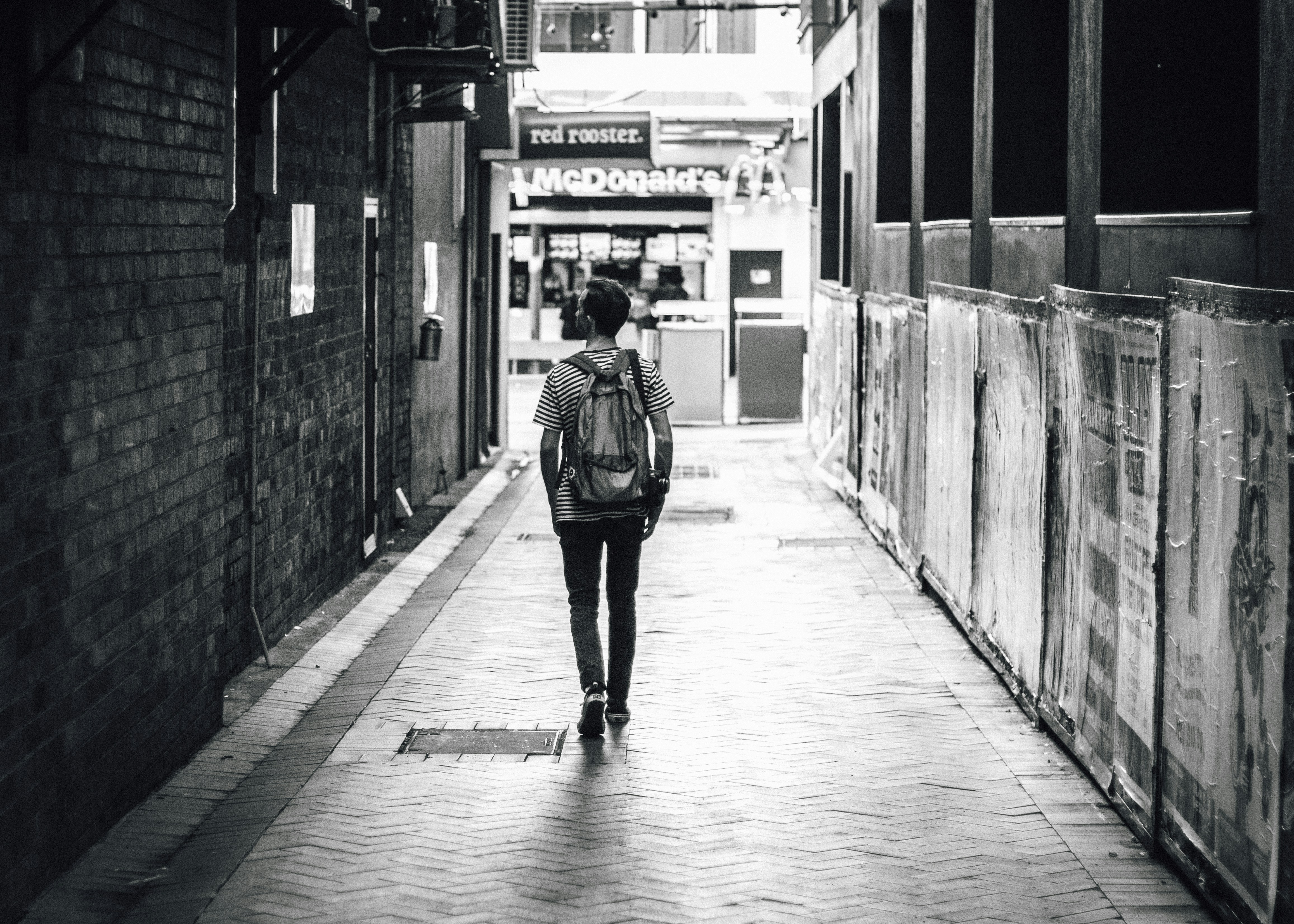 Black and white photo of a person walking through a narrow Brisbane alleyway with shops in the distance.