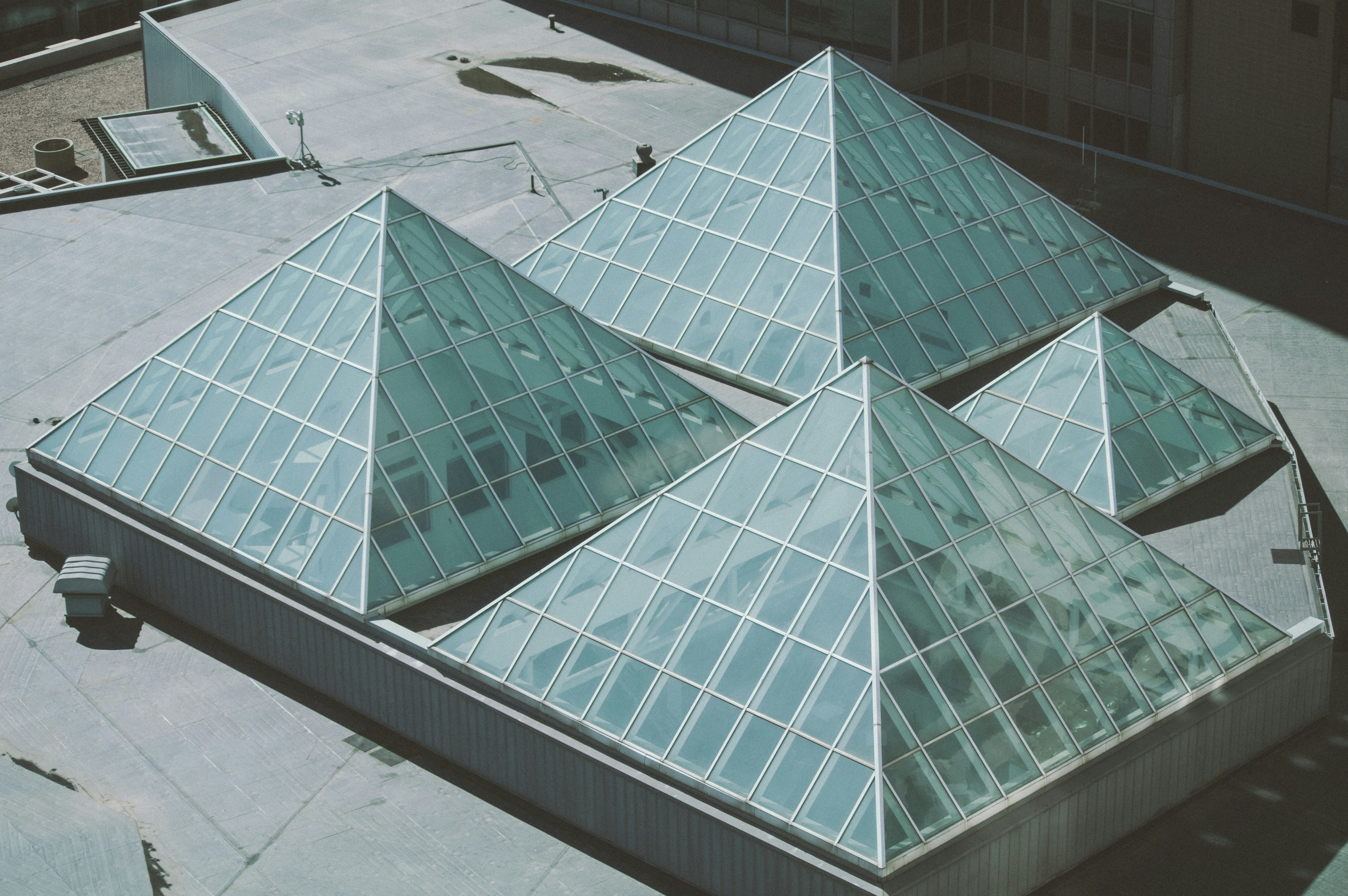 Four glass pyramids atop a modern building, showcasing a unique architectural design and reflecting sunlight. The symmetry and transparency create an intriguing visual effect.