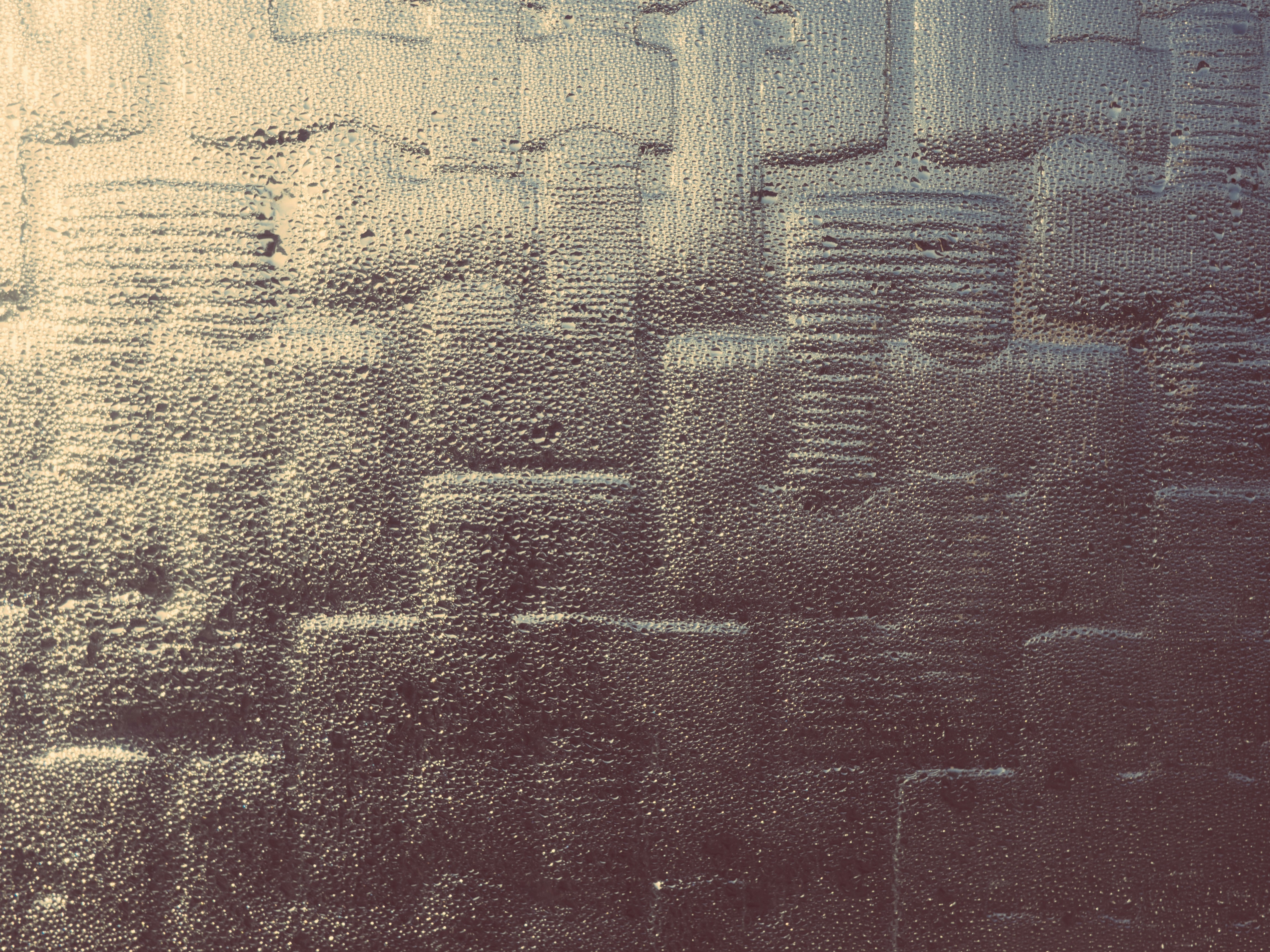 Condensation patterns on a glass surface create an abstract texture, evoking a sense of quiet morning atmosphere.