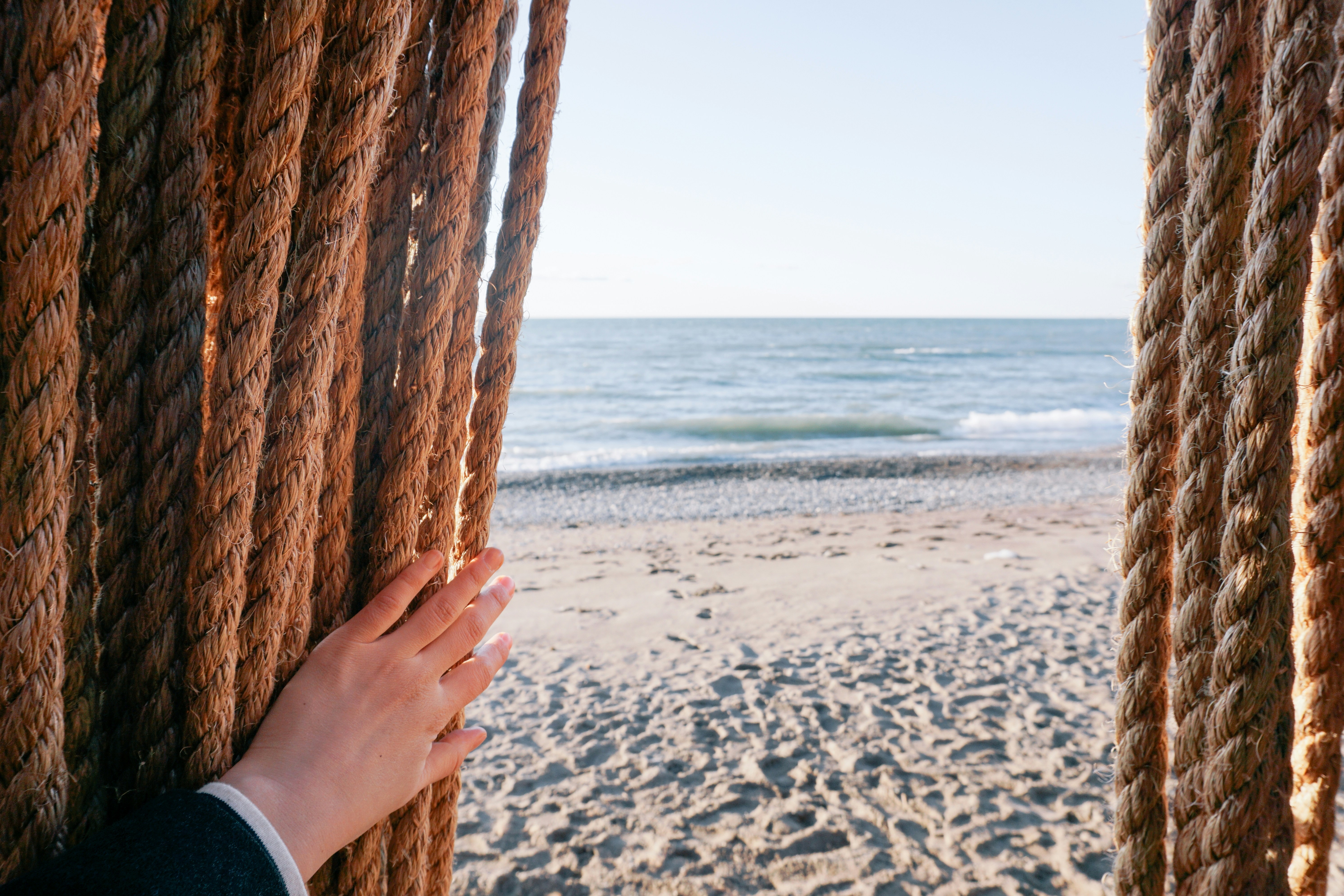 Hand gripping thick ropes on a sunny beach with gentle waves in the background.