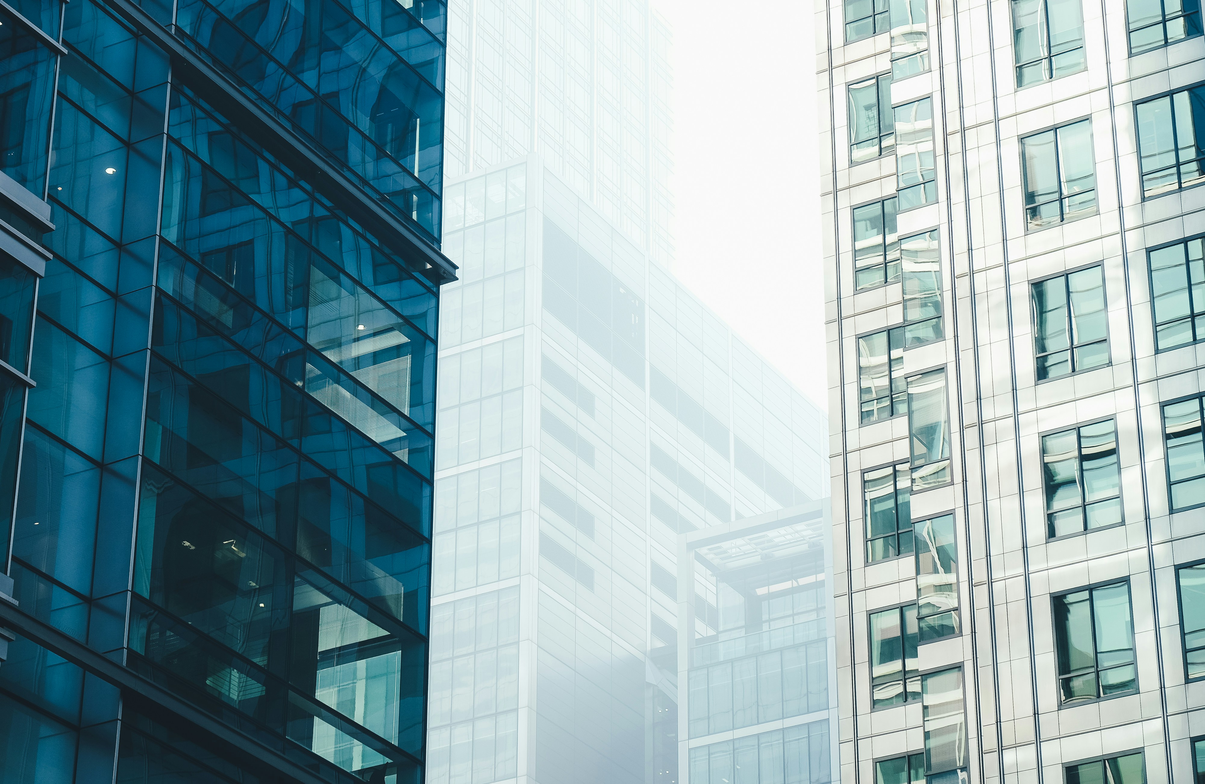 Abstract composition of modern skyscrapers with reflective glass facades, shrouded in mist. The interplay of light and shadow creates a dreamlike atmosphere.