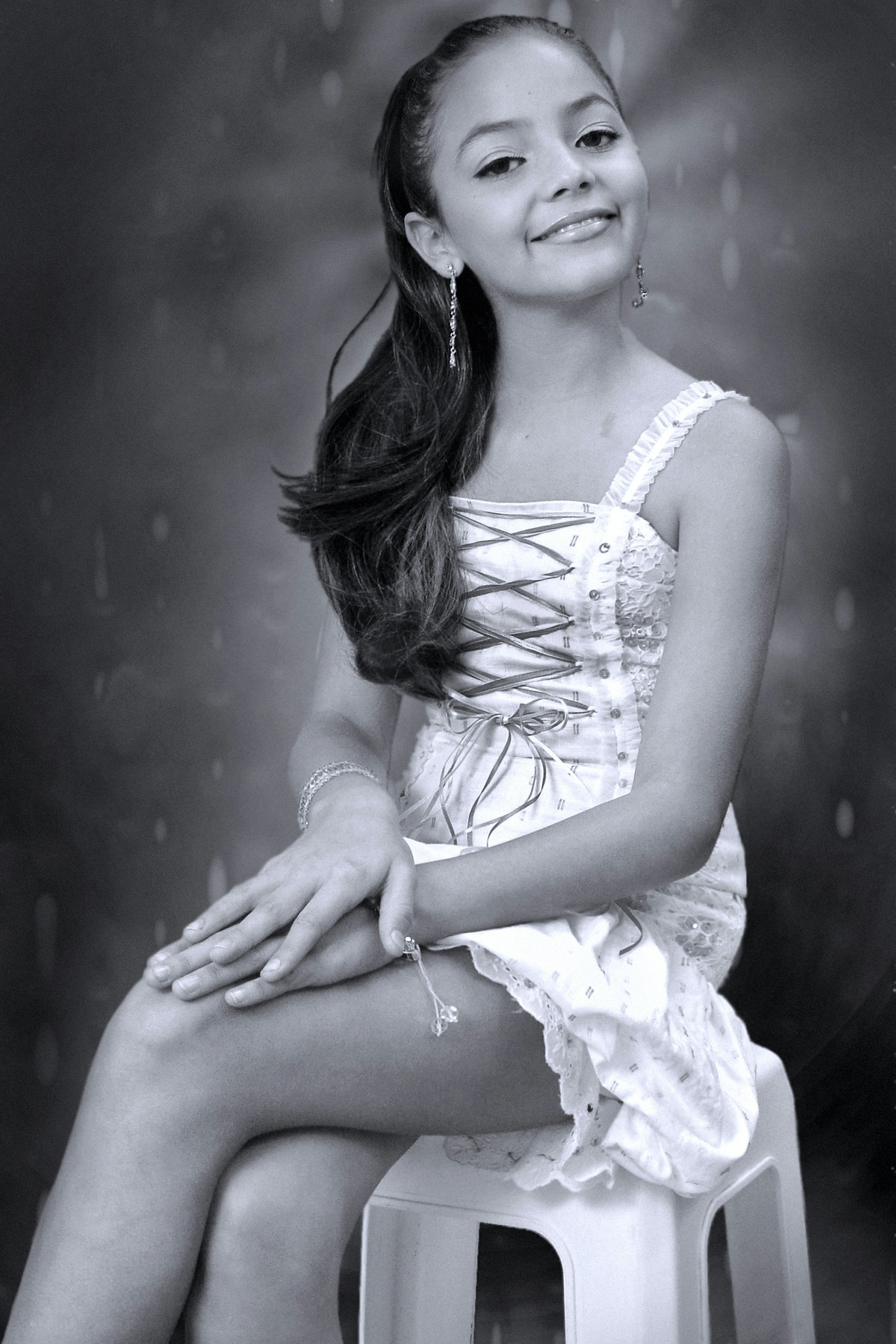 Young girl seated on a stool in a detailed dress, set against a softly blurred background.