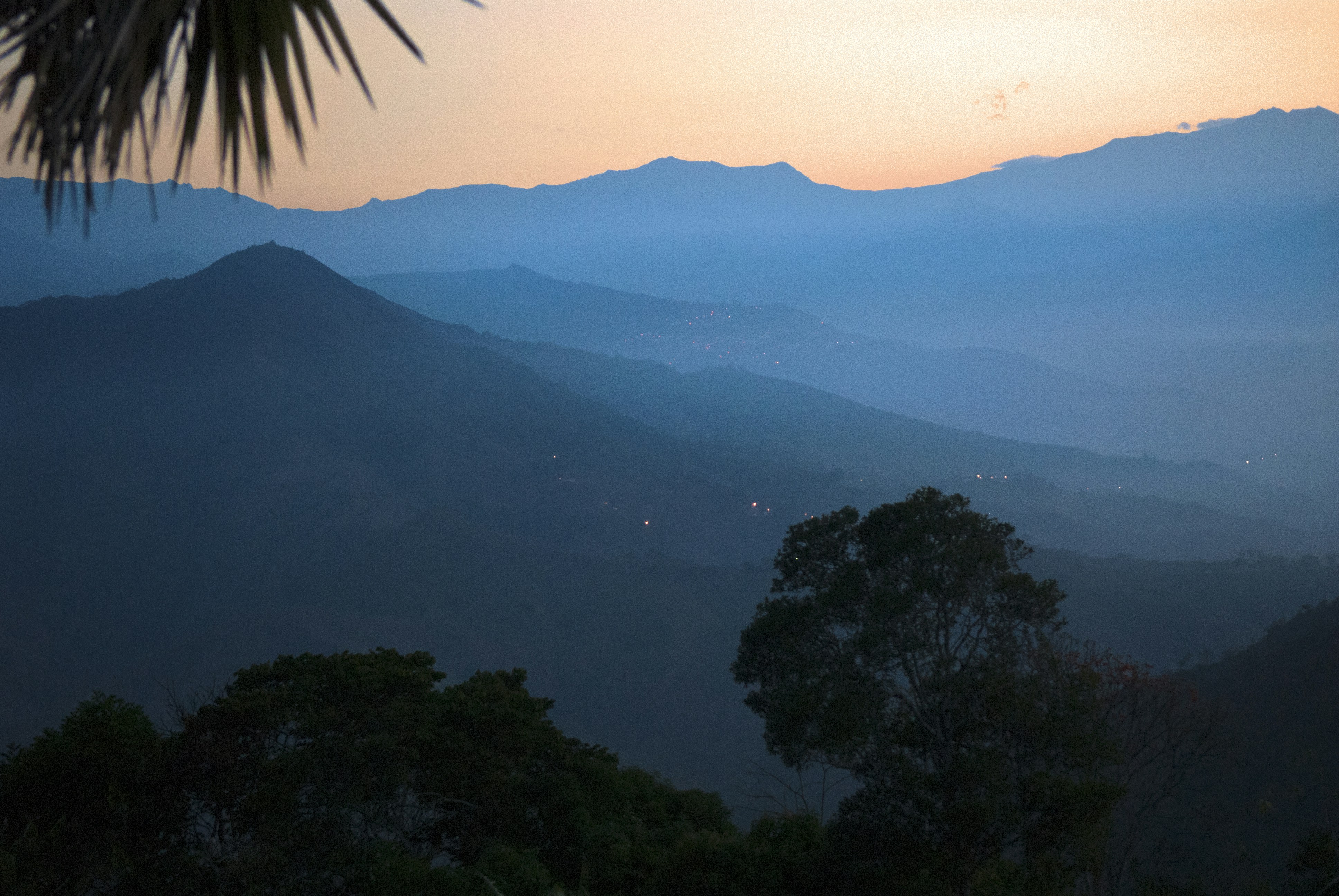 Silhouetted mountains under a soft sunrise glow, with misty layers descending into the valley below.
