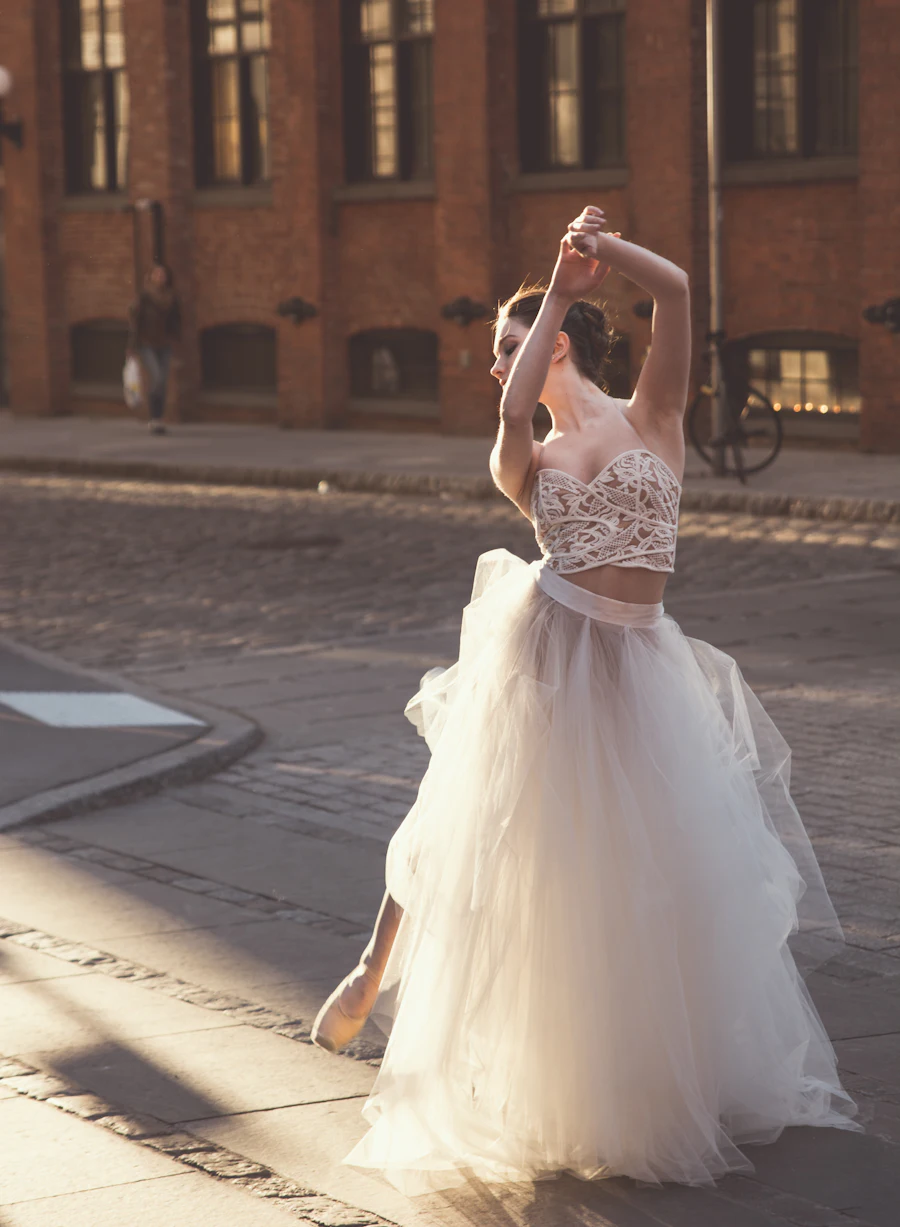A dancer in a flowing white gown gracefully twirls on a cobblestone street, illuminated by warm evening light.