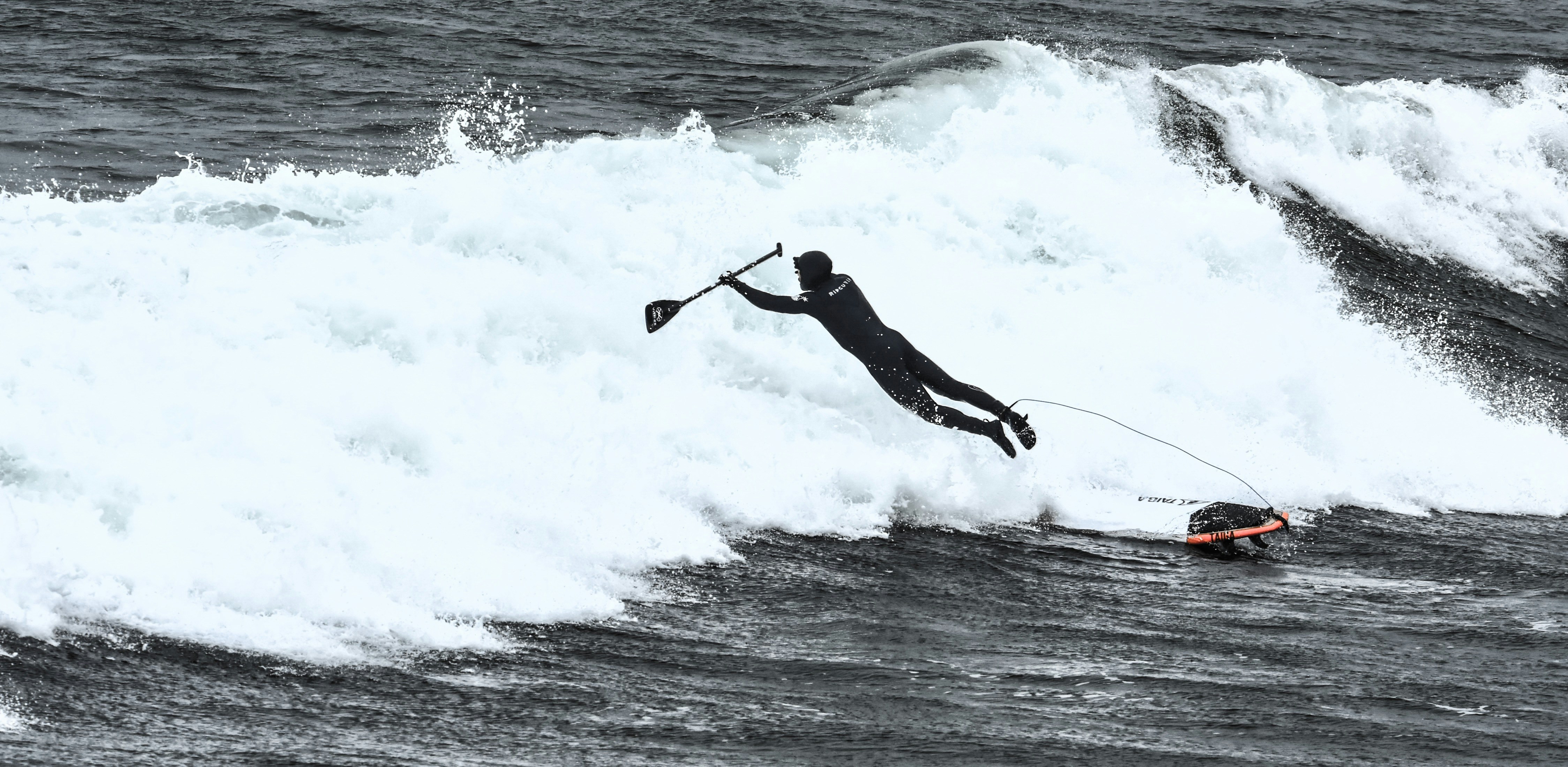Surfer mid-air above crashing waves, with board trailing behind.