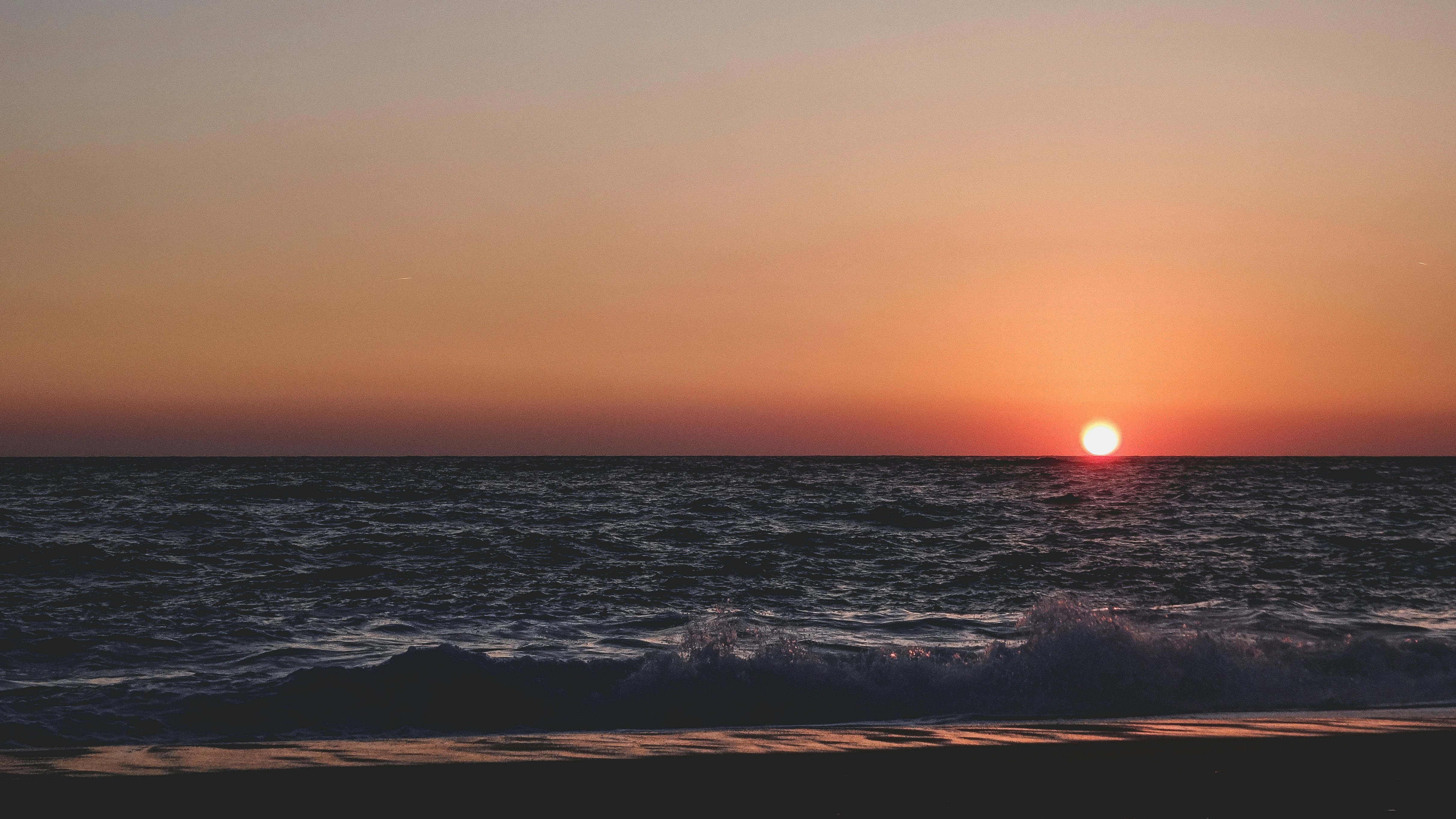 Sunset casting a warm glow over rippling ocean waves and a sandy shore.