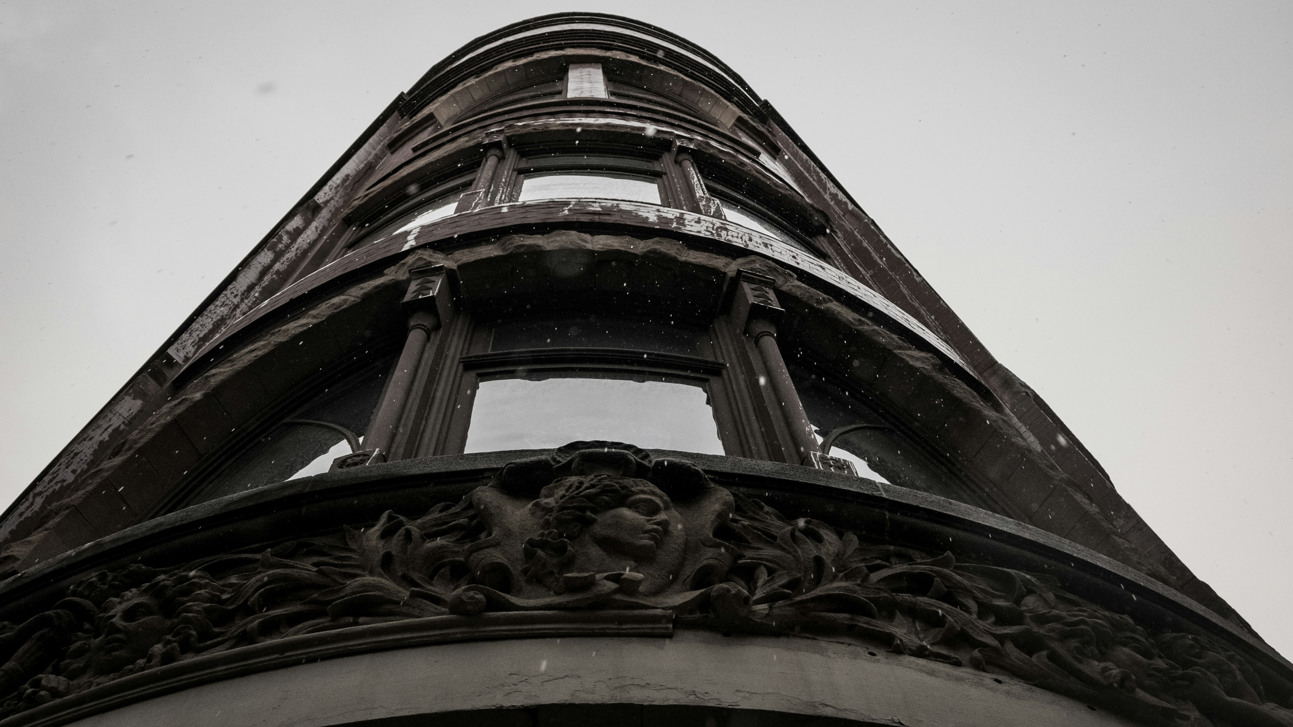 Worm's-eye view of a brown building with intricate stone carvings and falling snowflakes.