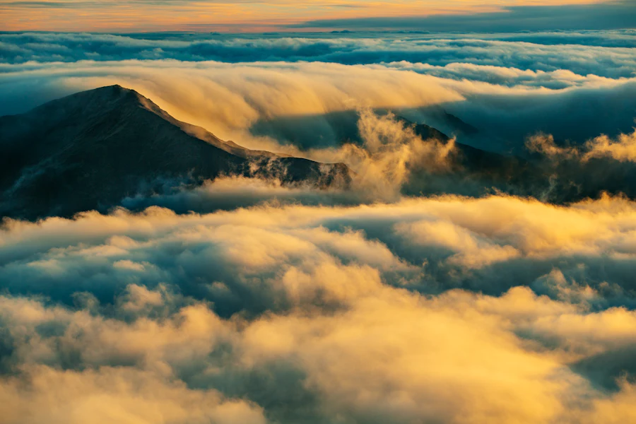 Mountain summit emerging from a sea of golden clouds at sunrise.