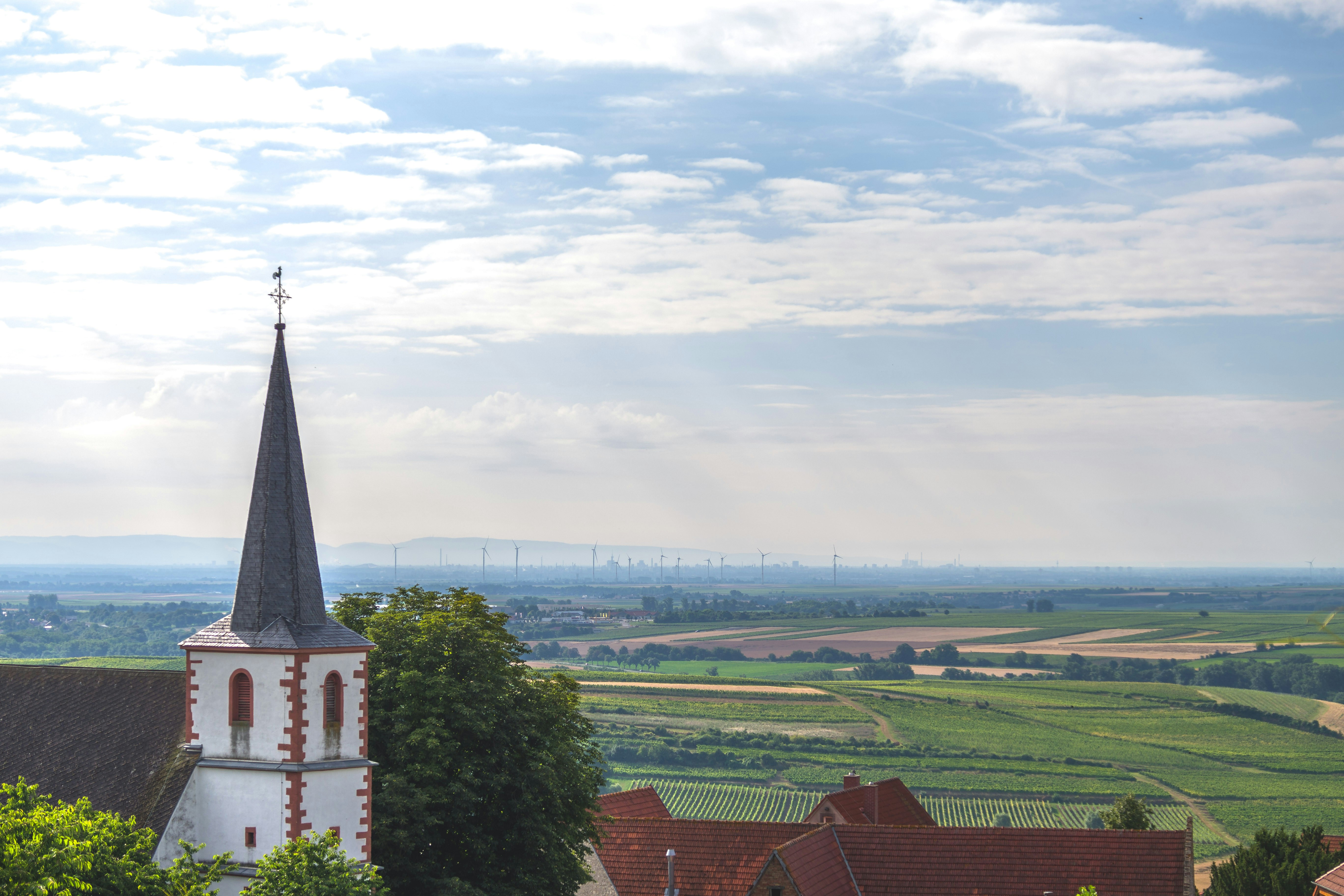 Church steeple rising above lush green fields and distant horizon under a partly cloudy sky.