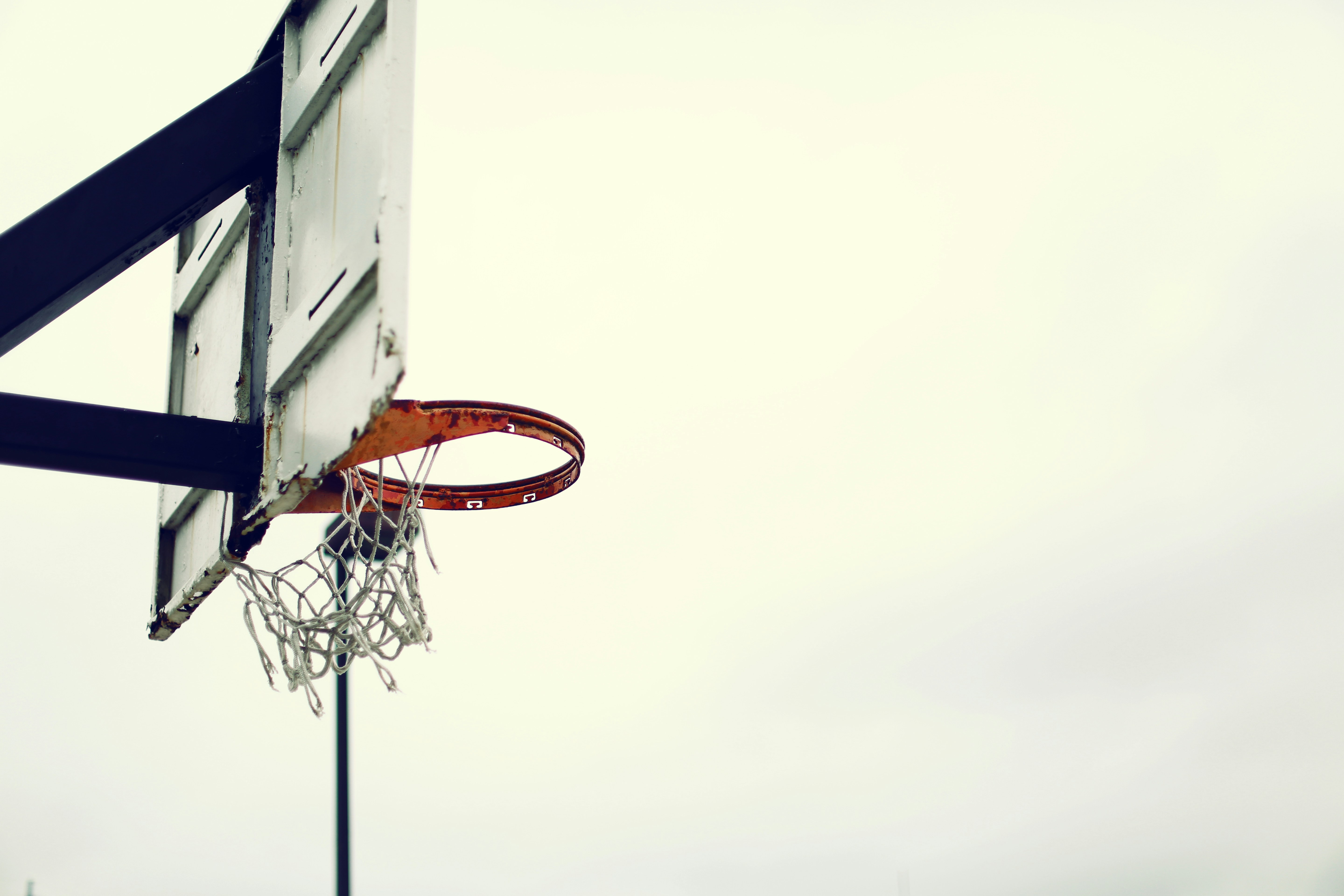 Portable basketball hoop with white backboard and red rim against an overcast sky.