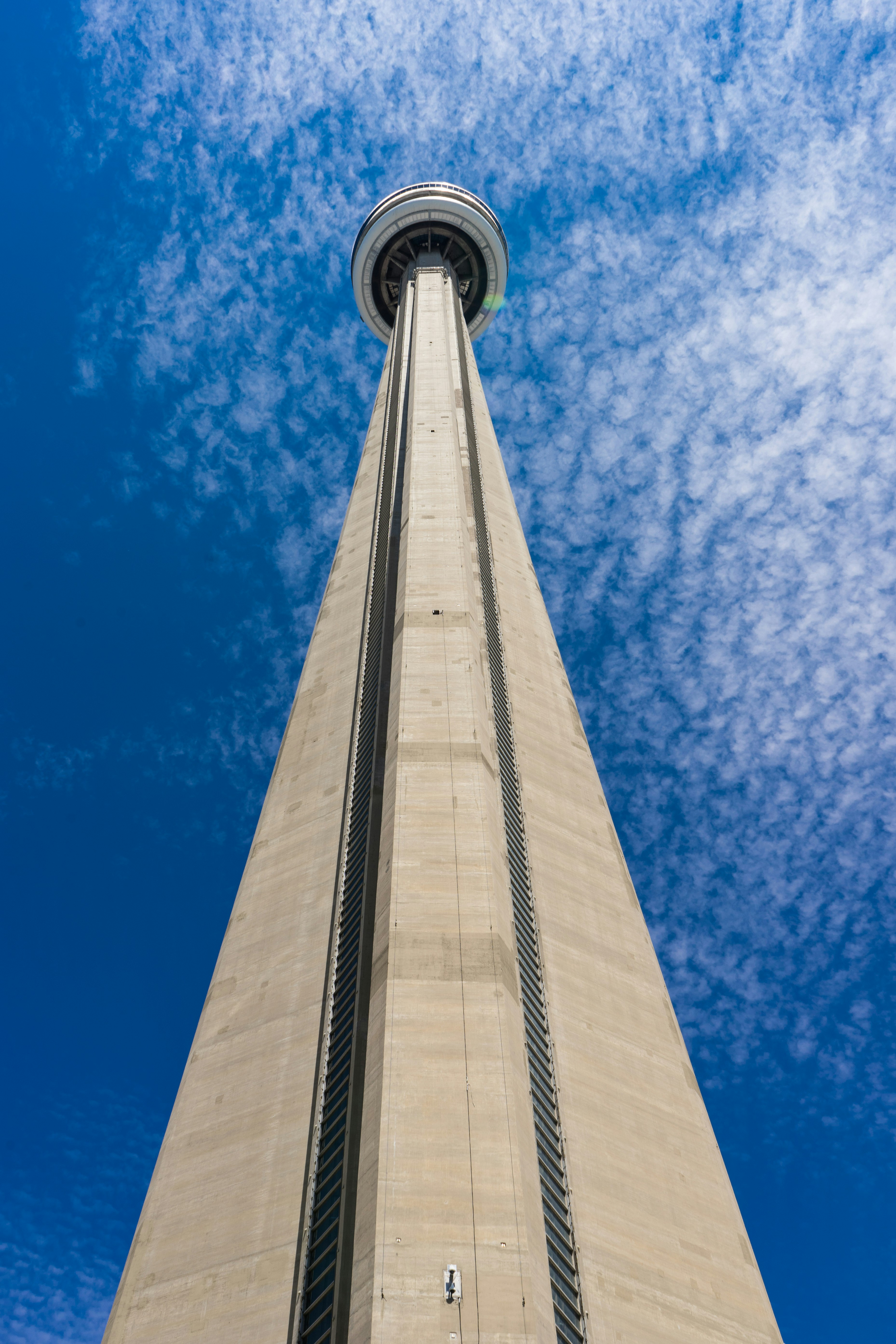 Low angle view of a towering concrete structure reaching into a sky filled with scattered, wispy clouds.