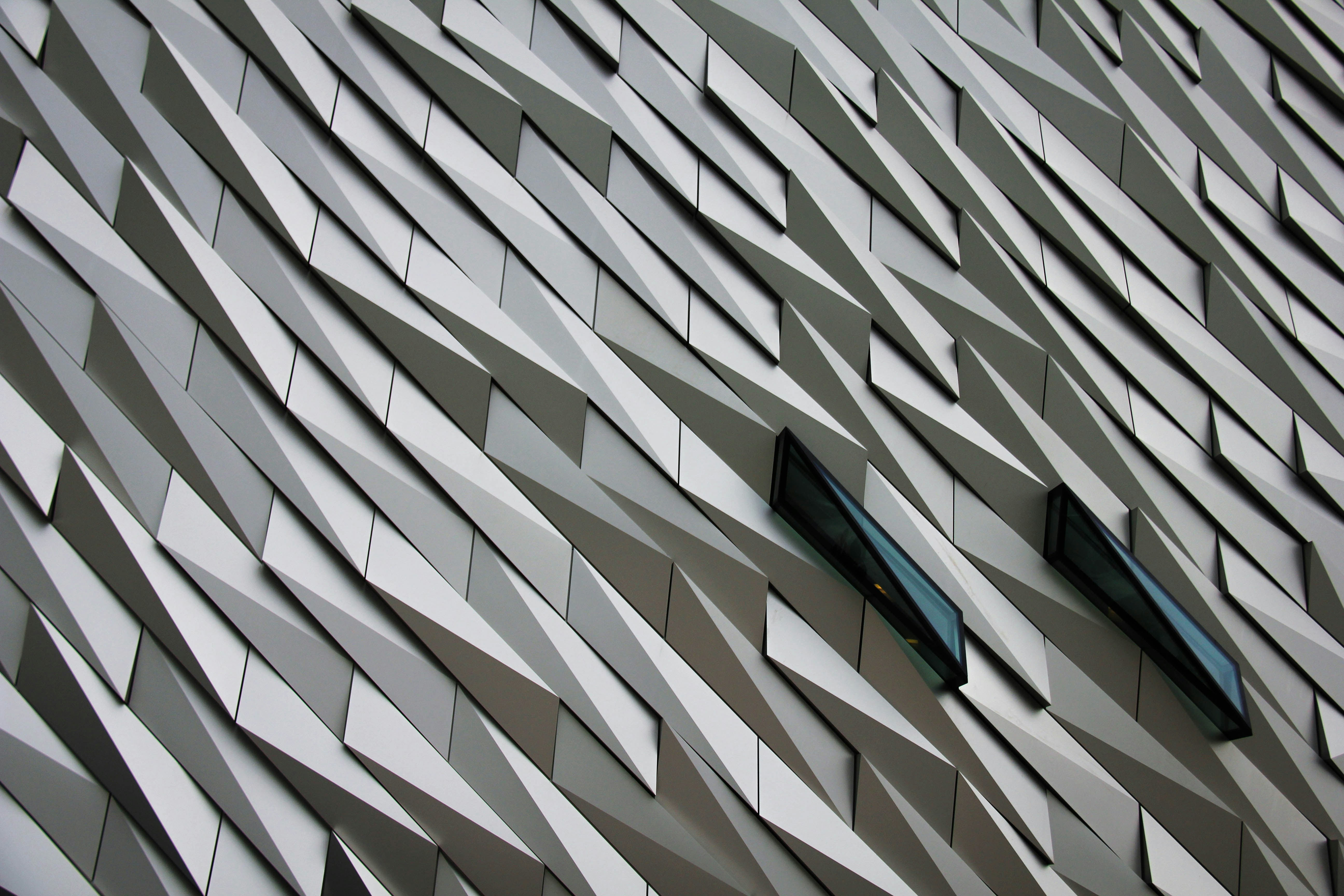 Abstract architectural detail featuring a dynamic wave pattern of gray and white panels with two protruding windows. 