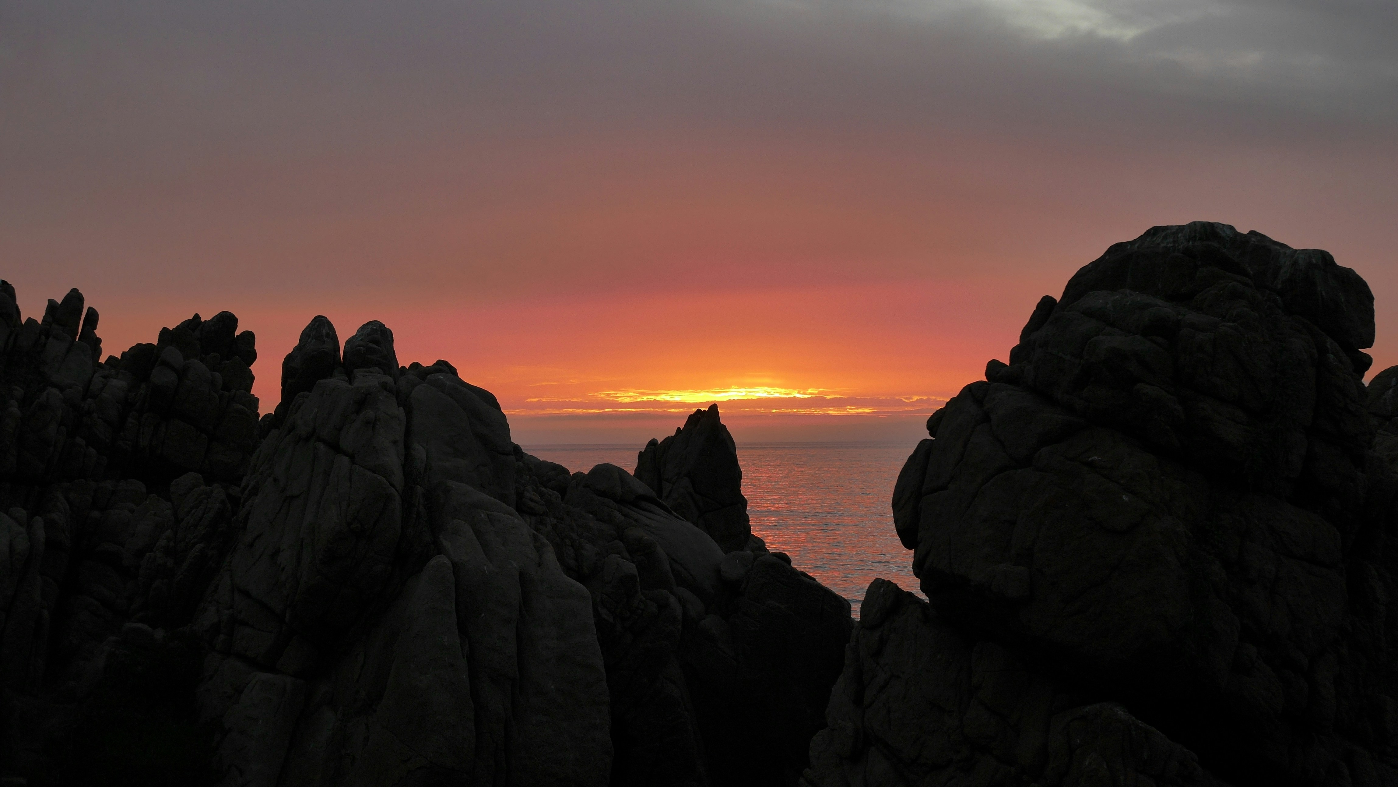 Sunset casts a warm glow over jagged rock formations against a serene sea horizon.