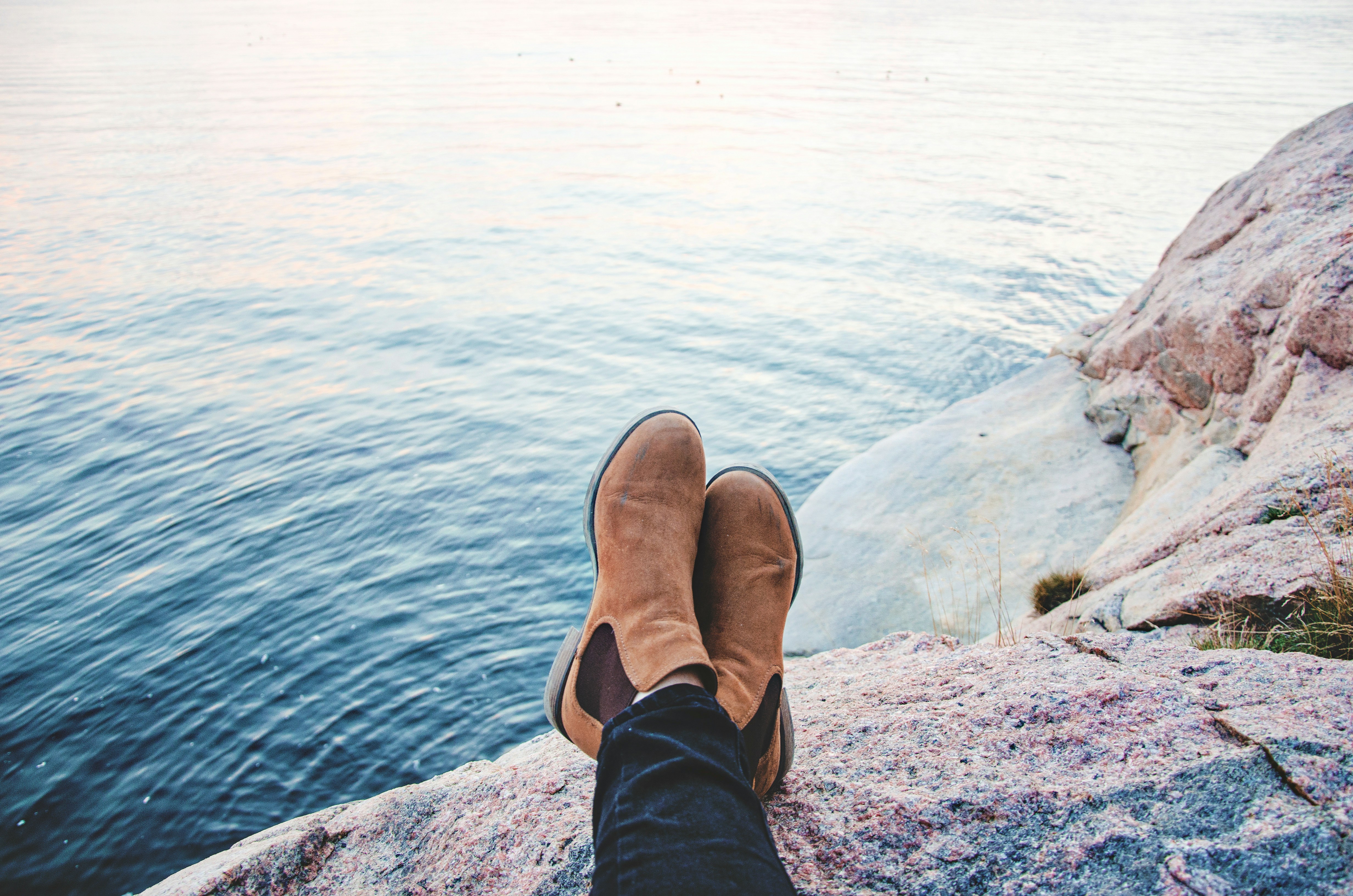 A pair of brown boots resting on a rocky ledge overlooking calm waters, capturing a moment of tranquility in nature.