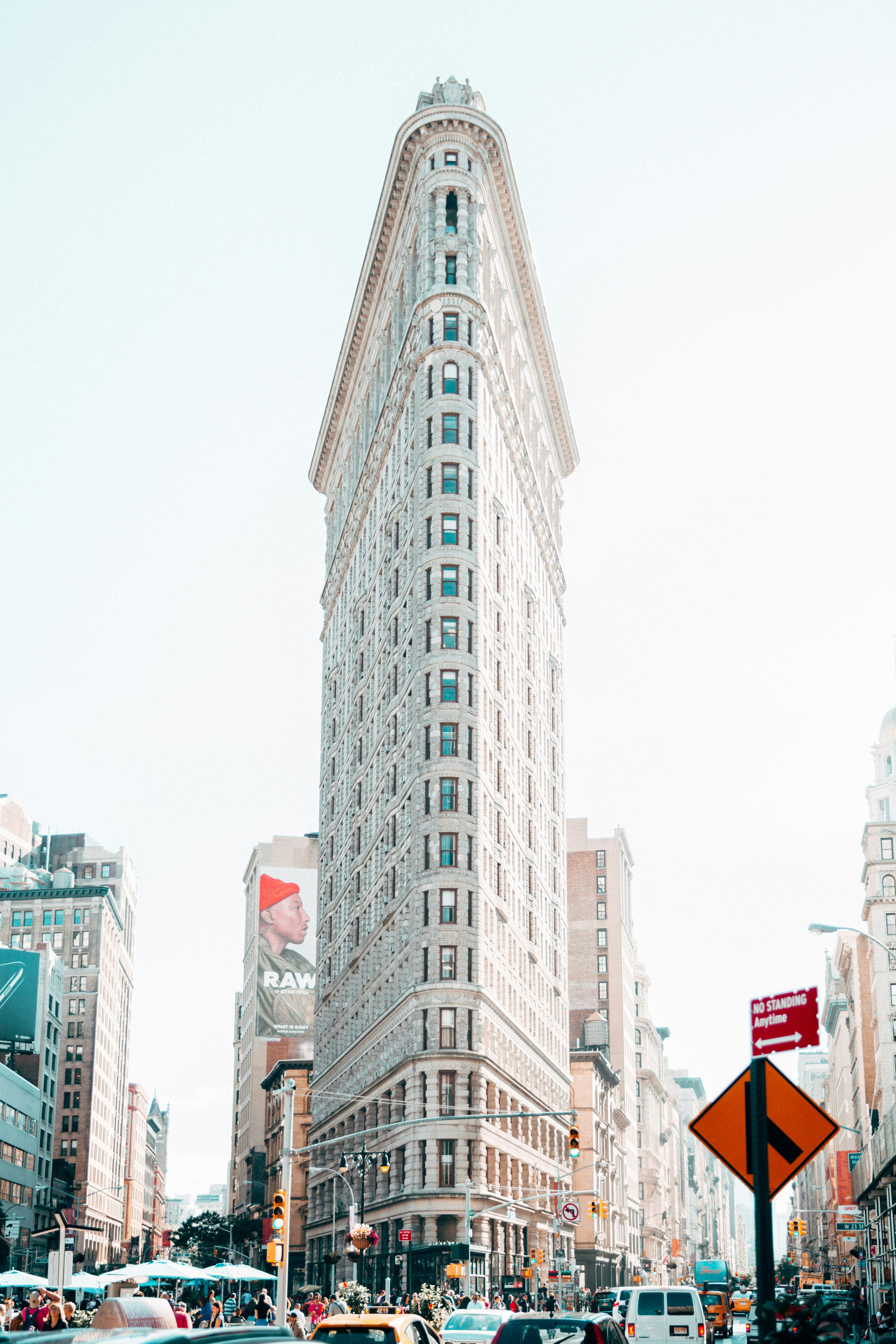 The Flatiron Building stands tall amidst the bustling city, showcasing its unique triangular shape and architectural details. A vibrant urban scene unfolds at its base.
