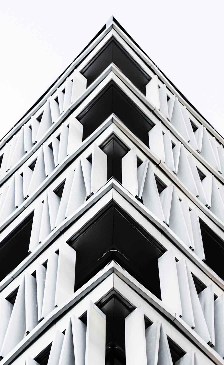 Geometric concrete facade forming diagonal stacked diamonds along a sharp corner; the image emphasizes the building's repetitive angular pattern against a pale sky.