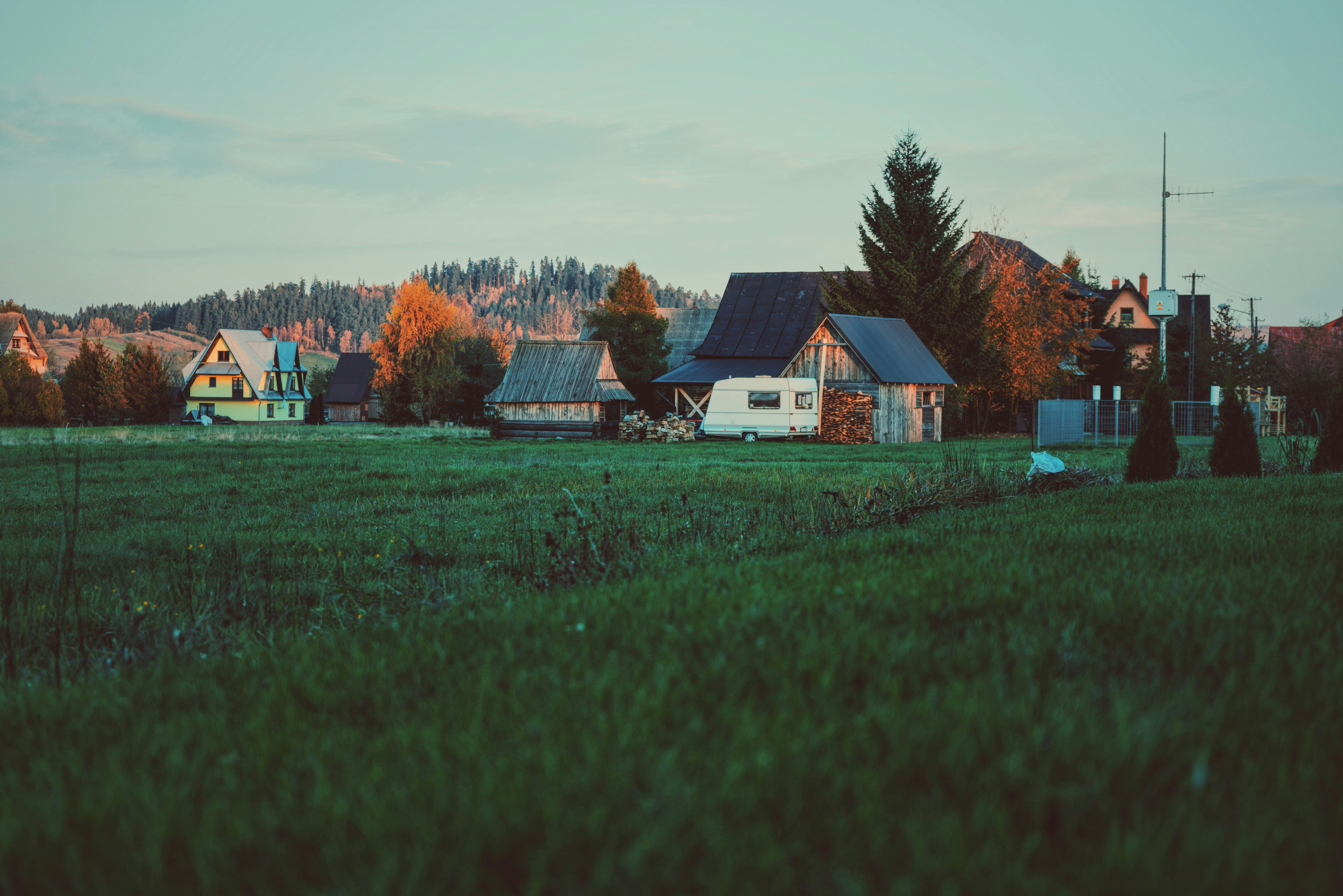Cluster of houses nestled in a serene field at dusk with hills in the background.