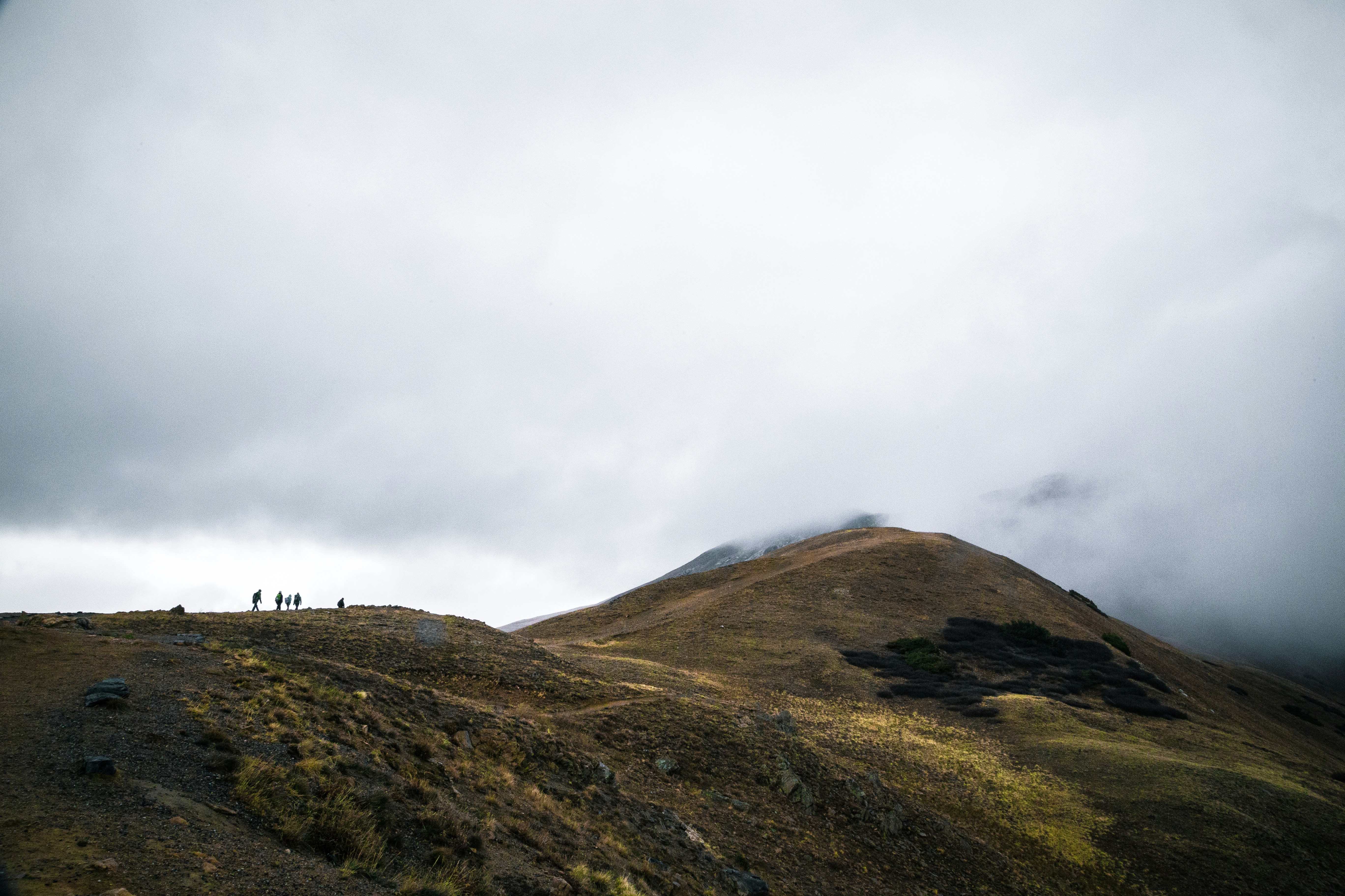 Silhouetted figures traverse a rugged hillside under a moody, overcast sky, evoking a sense of adventure and solitude.