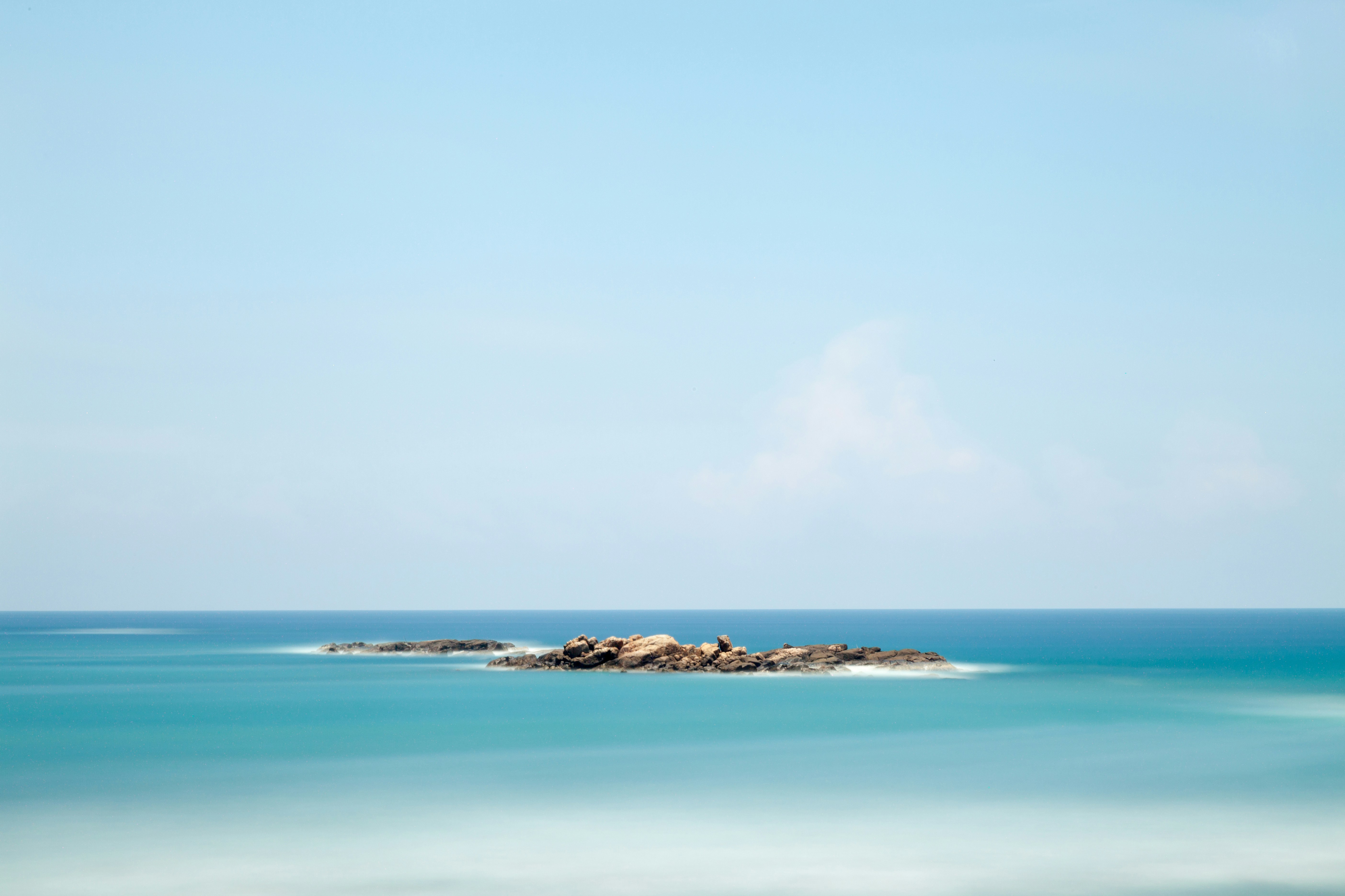Rocky islet surrounded by smooth, turquoise sea under a clear blue sky.
