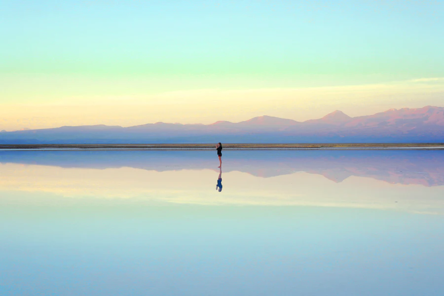 Woman taking a picture in the middle of a "salar"/lake in the dessert of Atacama, Chile. | person standing near body of water during daytime