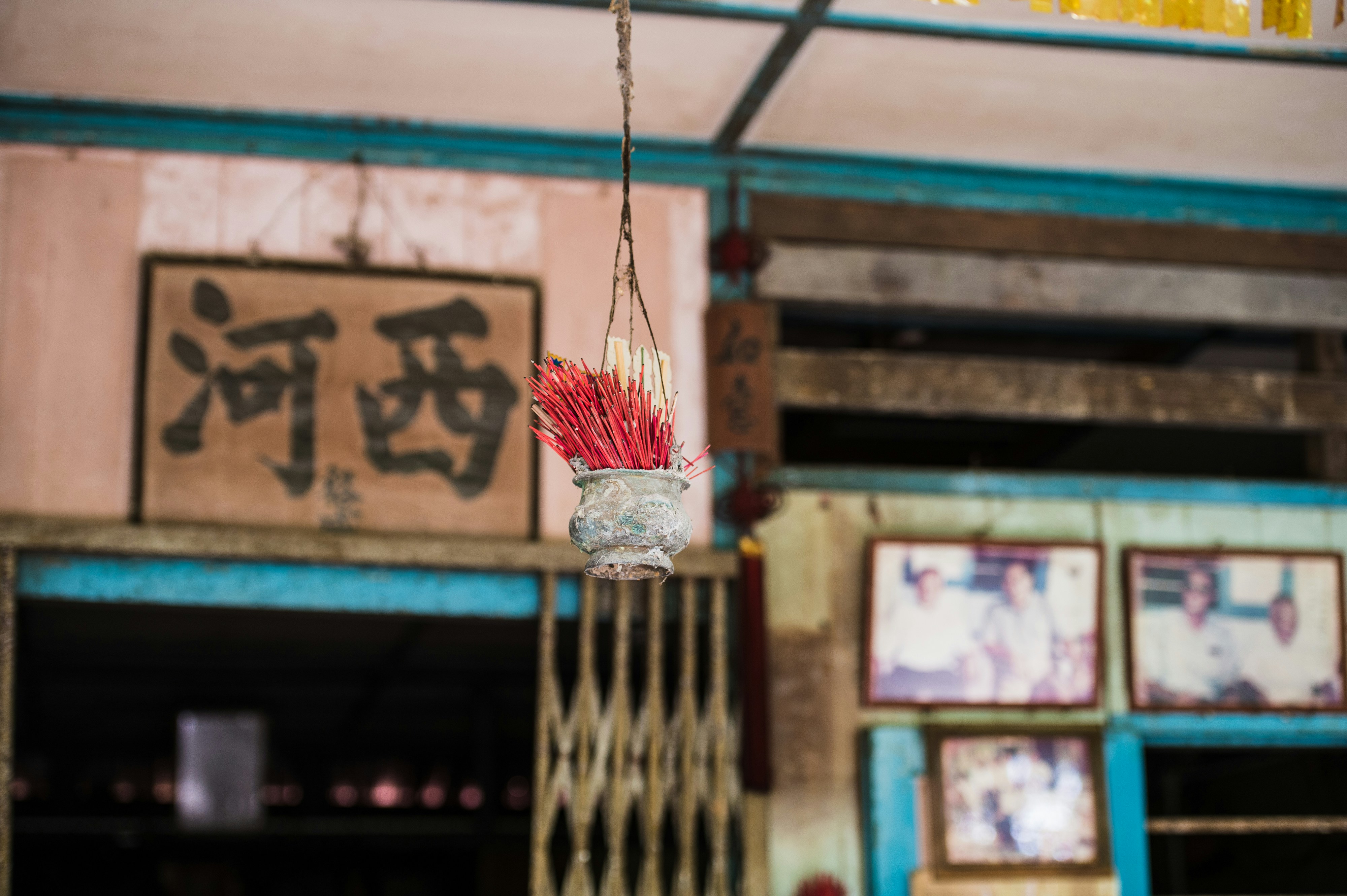 Hanging incense sticks in a glass holder, set against a backdrop of historical photographs and a calligraphic sign. The scene reflects a rich cultural heritage.