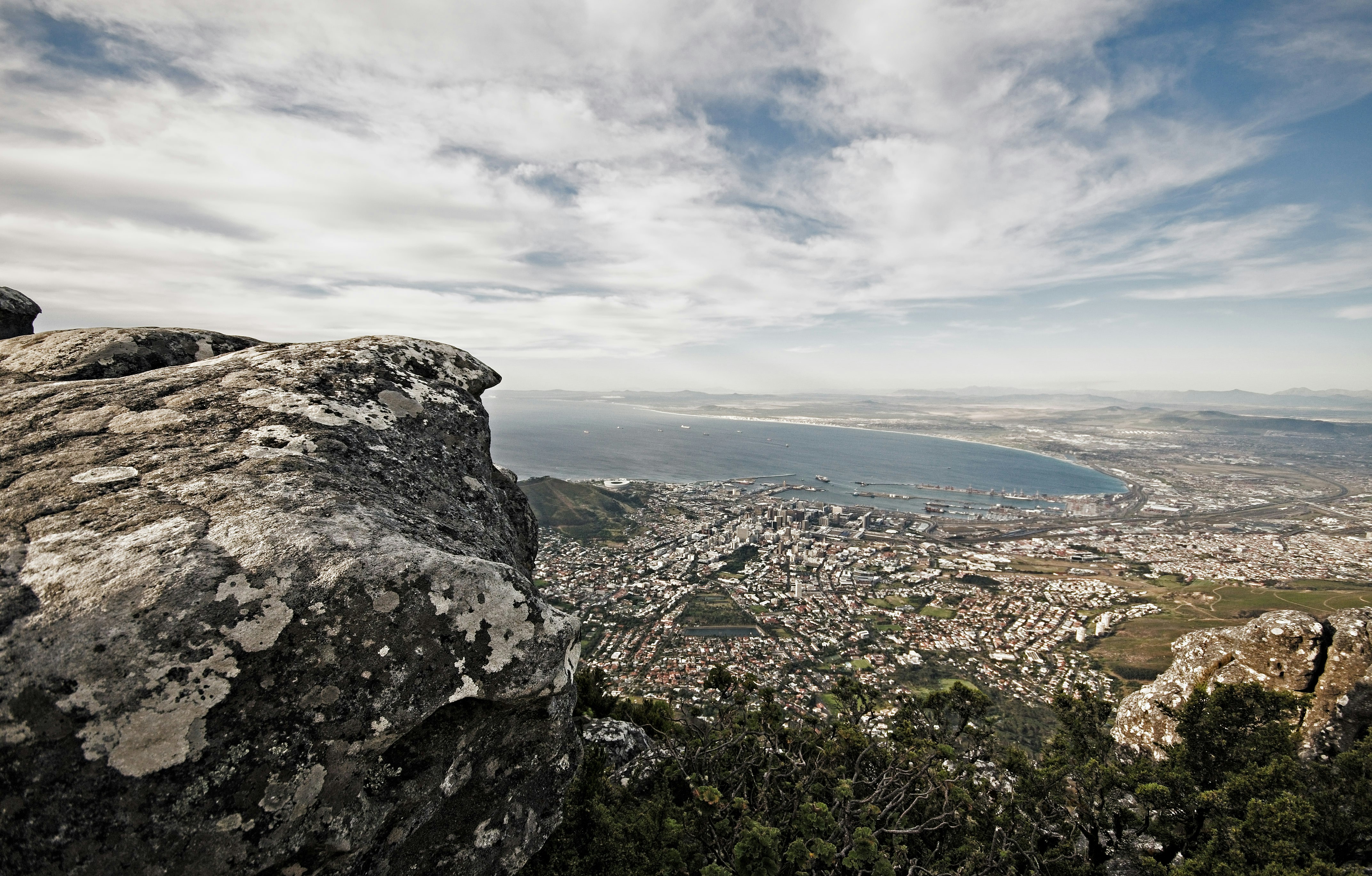 Vast view from a rocky vantage point, revealing a sprawling coastal city and the shimmering ocean beyond.