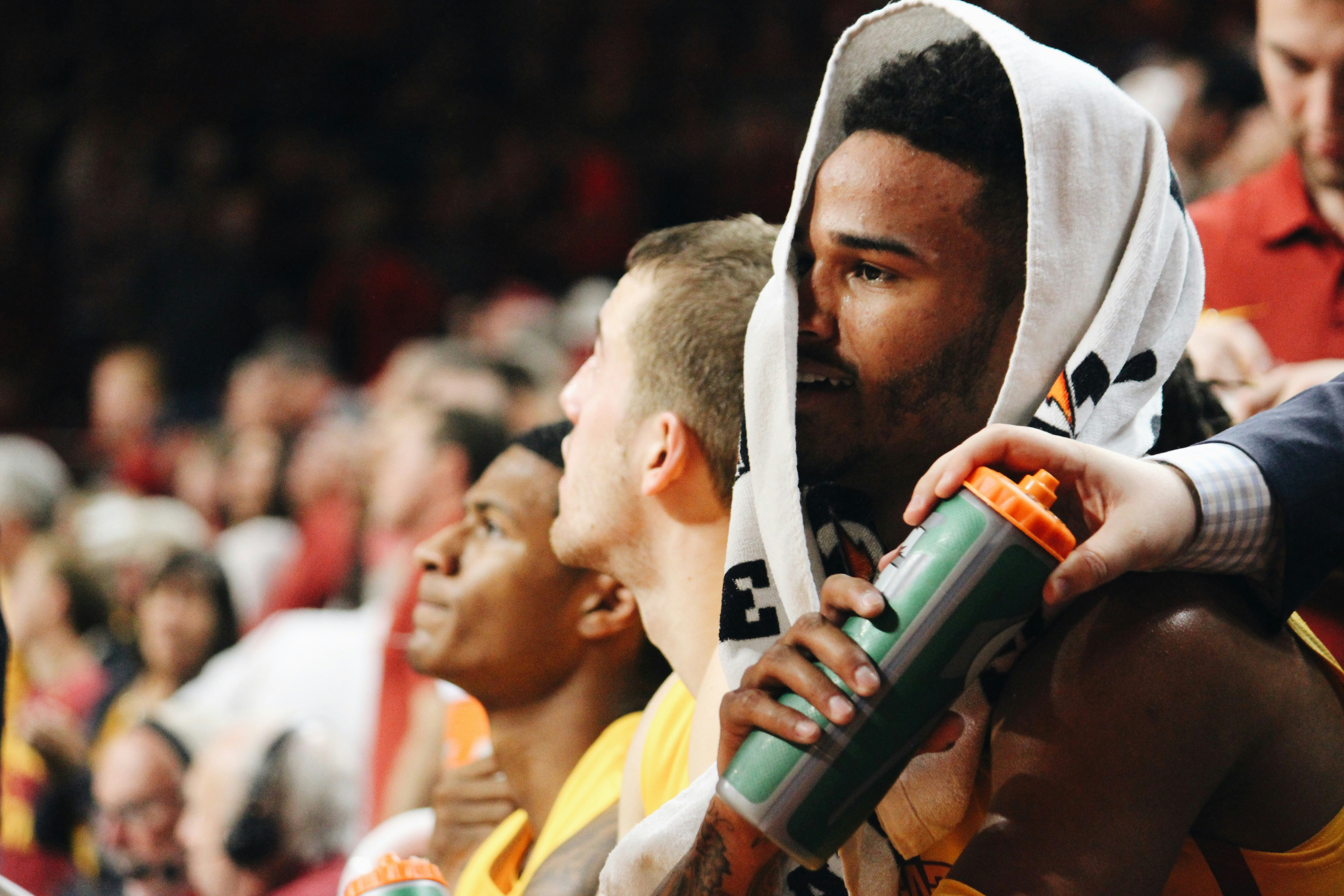 Basketball player with a towel draped over his head, holding a green tumbler during a game.