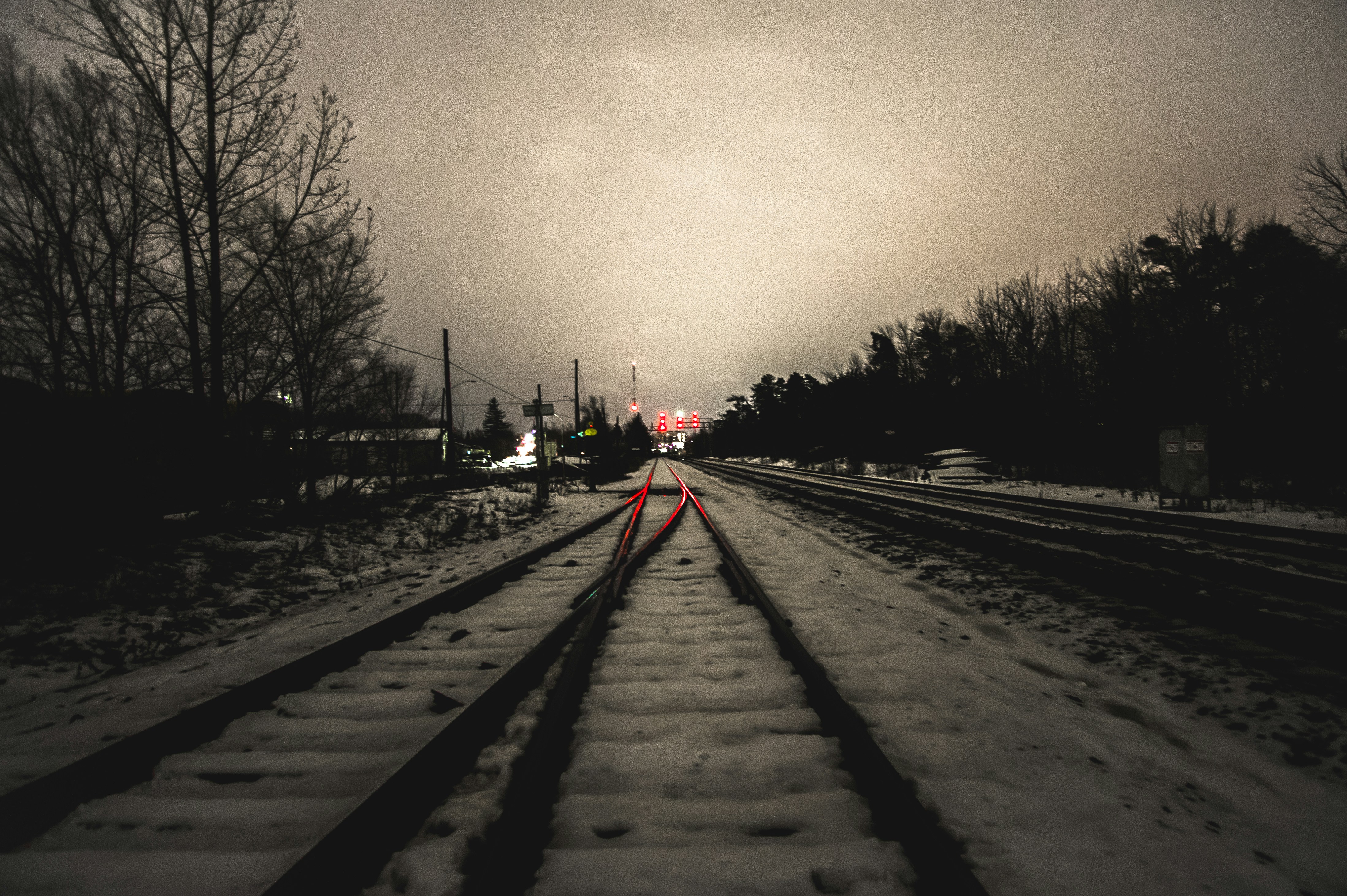 Snow-covered railroad tracks converge toward a distant red signal beneath a muted winter sky.