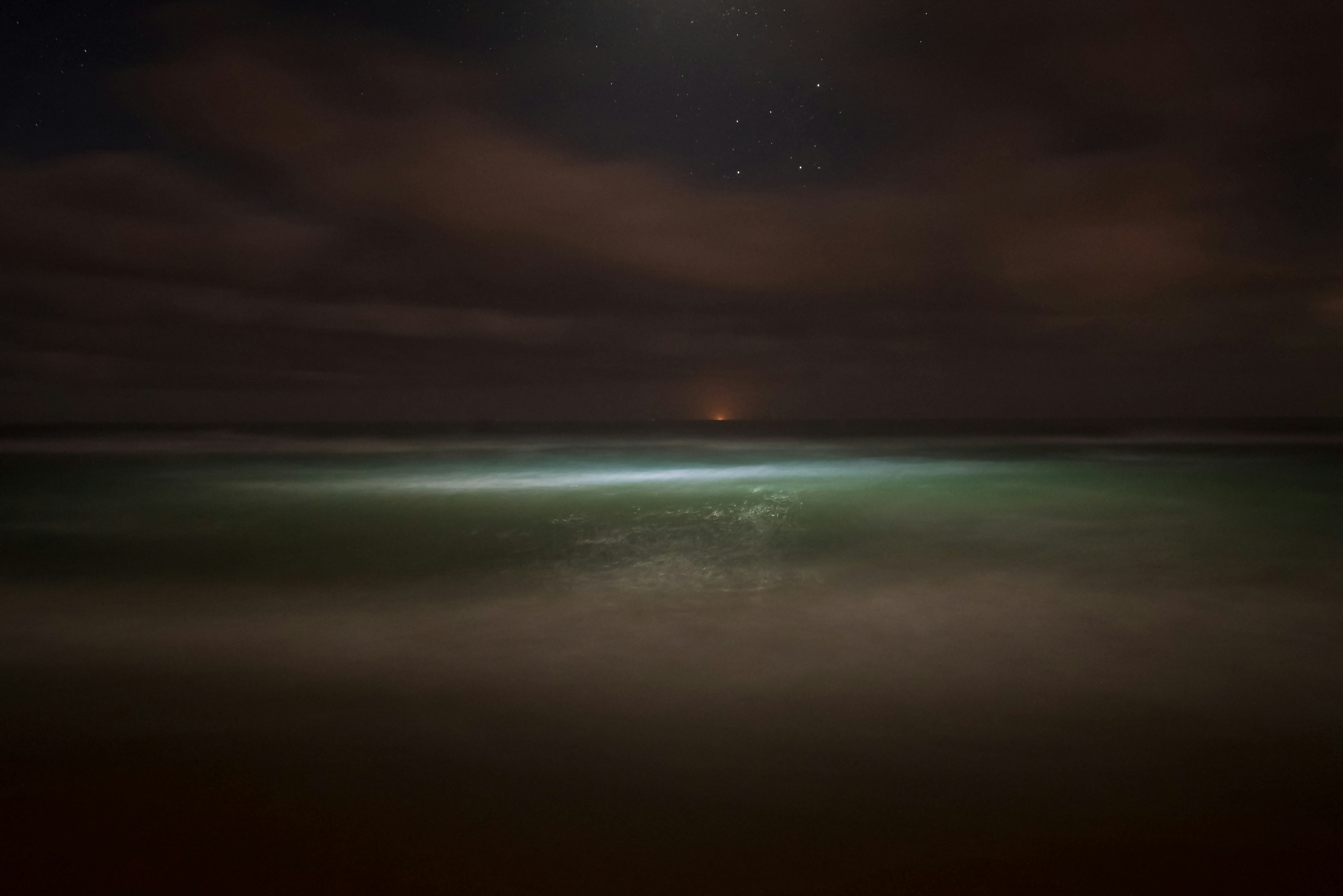 Softly illuminated ocean waves under a starry night sky with subtle moonlight.