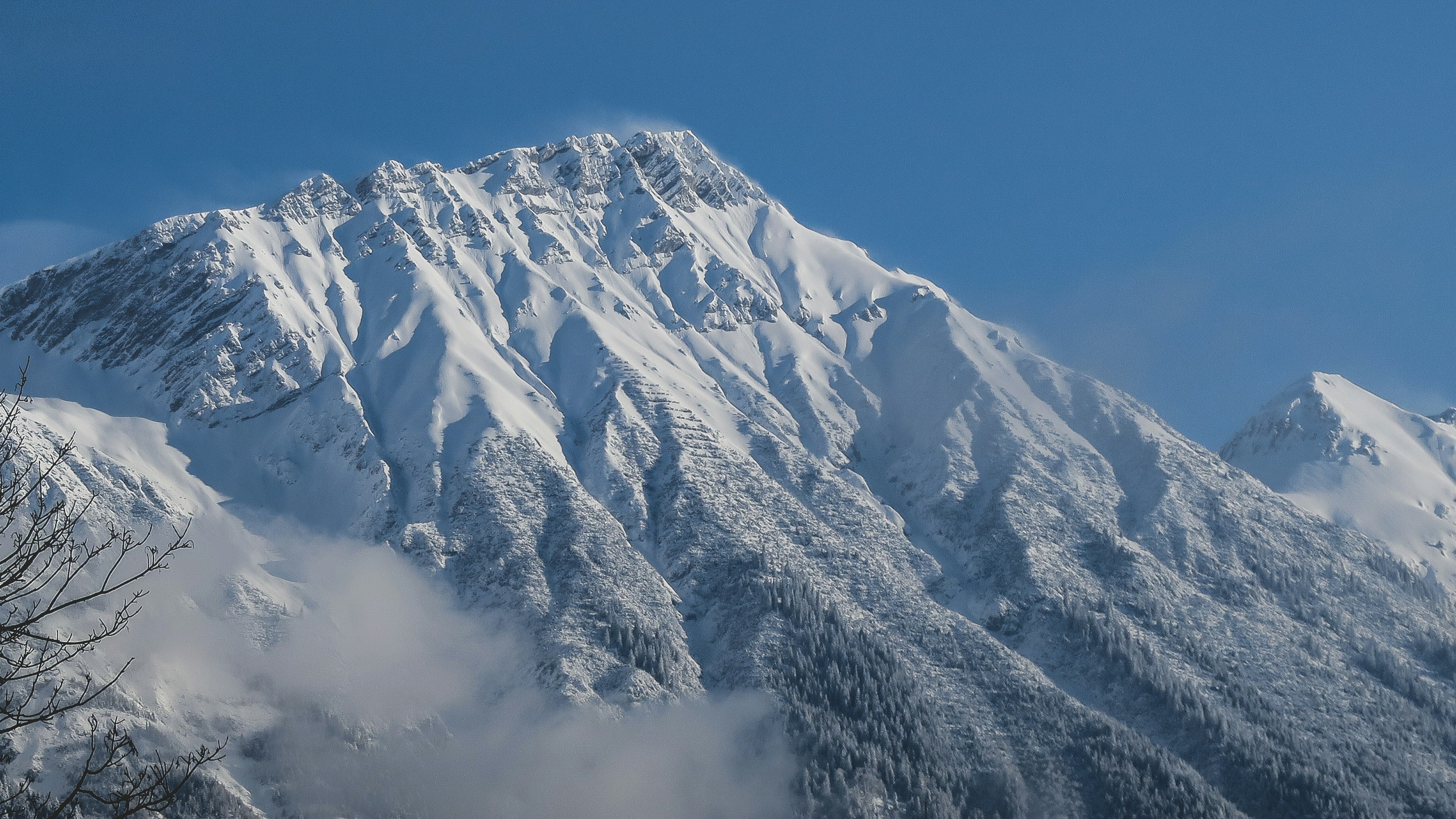 Snow-covered mountain peak with sharp ridges under a bright blue sky.