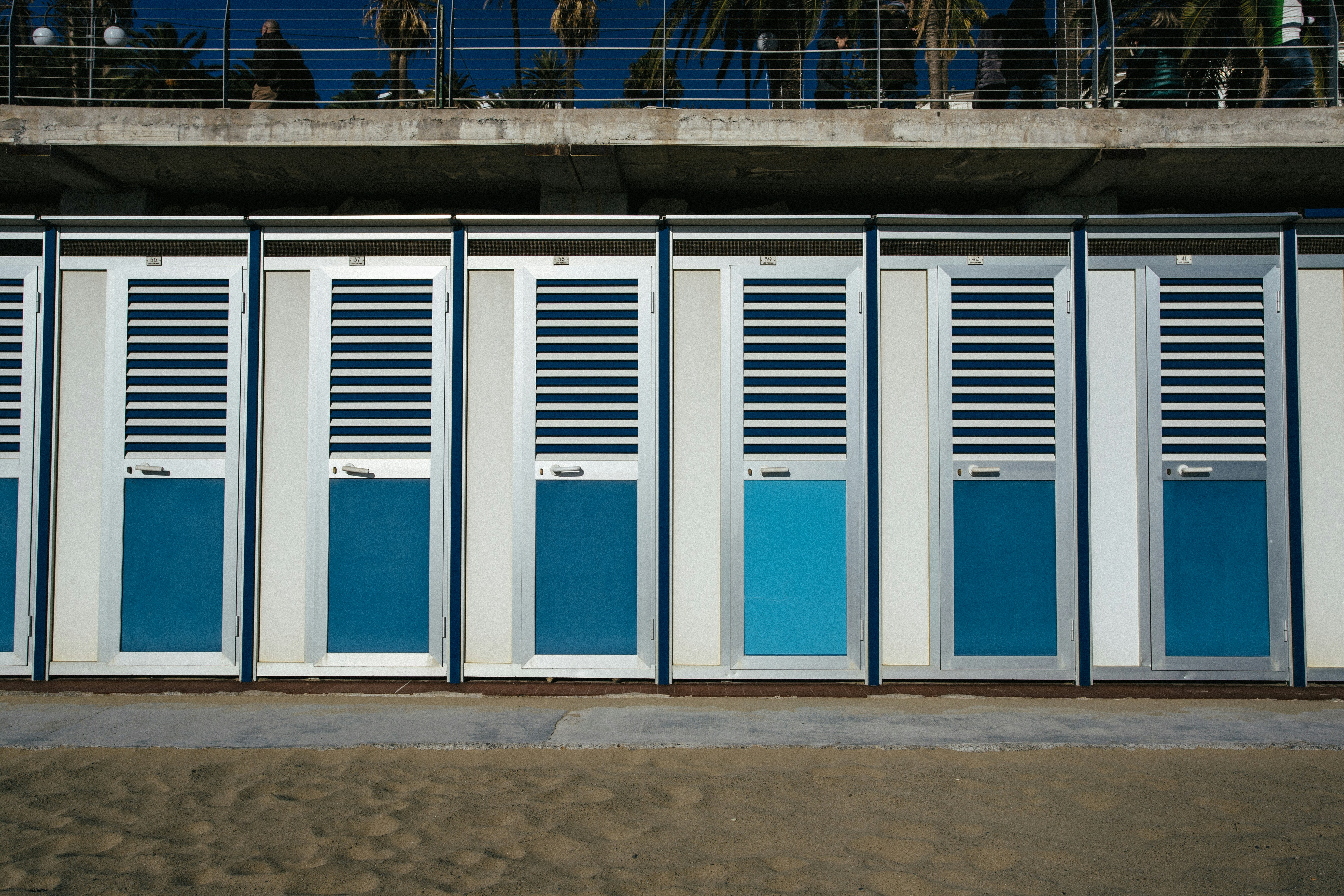 Symmetry in Azure: A Row of Beach-Blue Doors Beneath a Sunlit Promenade