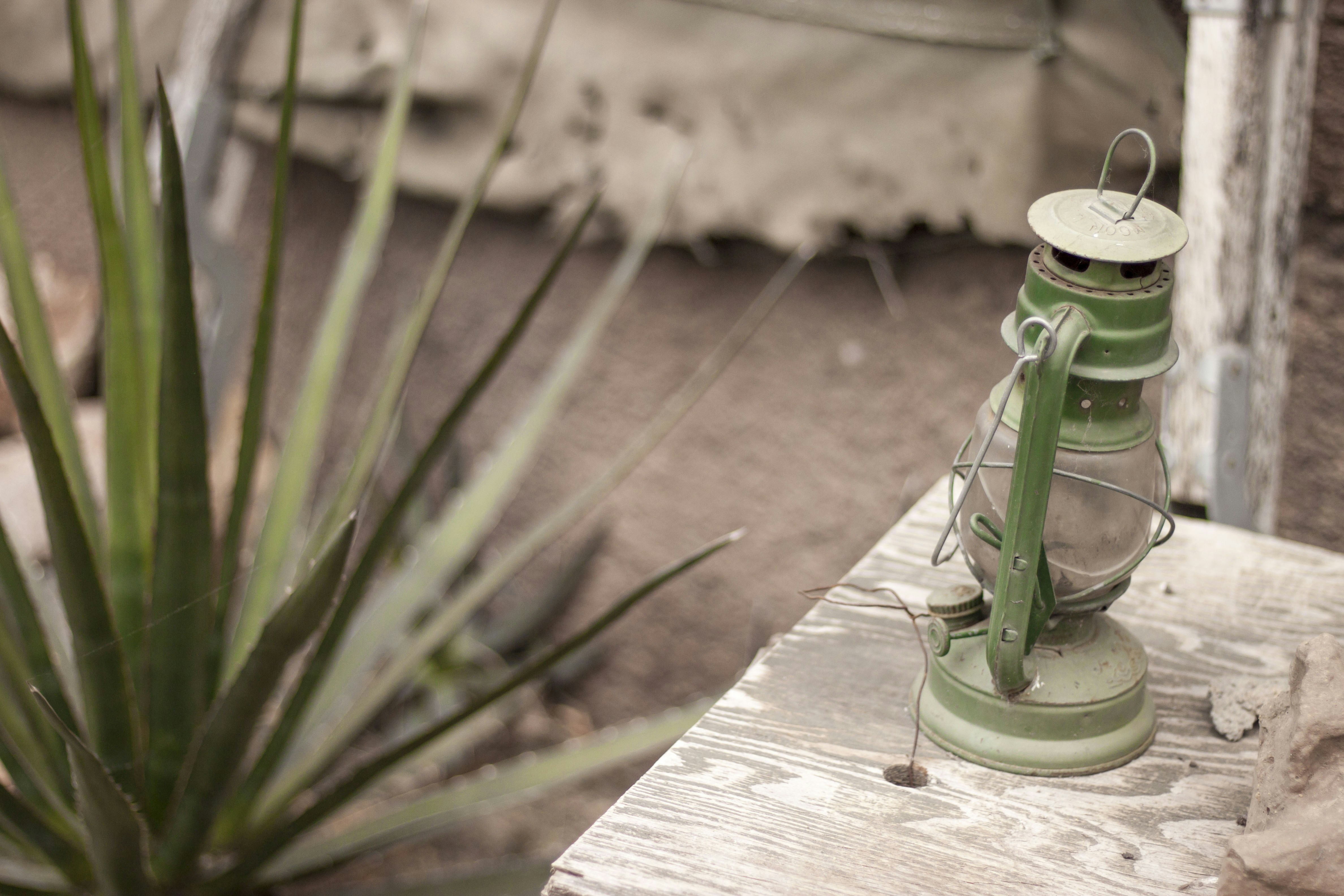 Rustic green lantern resting on a weathered wooden table, surrounded by desert flora. The scene evokes a sense of nostalgia and simplicity.
