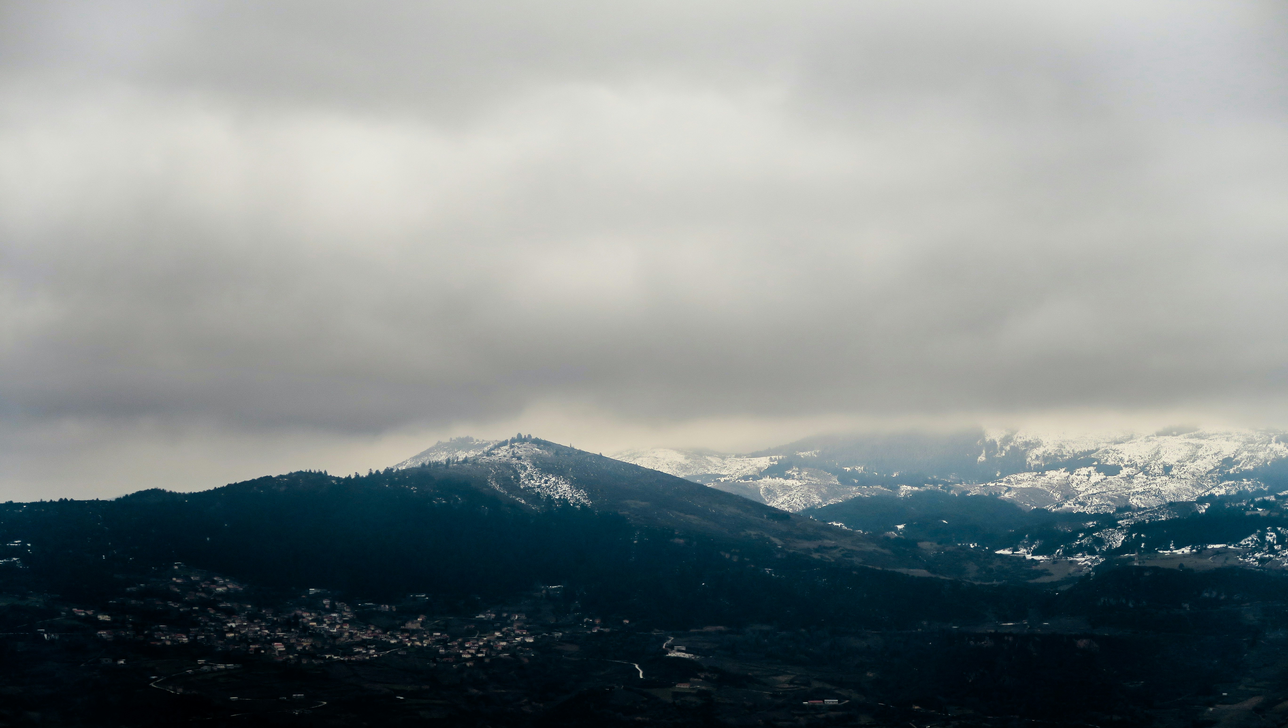 Snow-dusted mountains beneath a blanket of thick, gray clouds.
