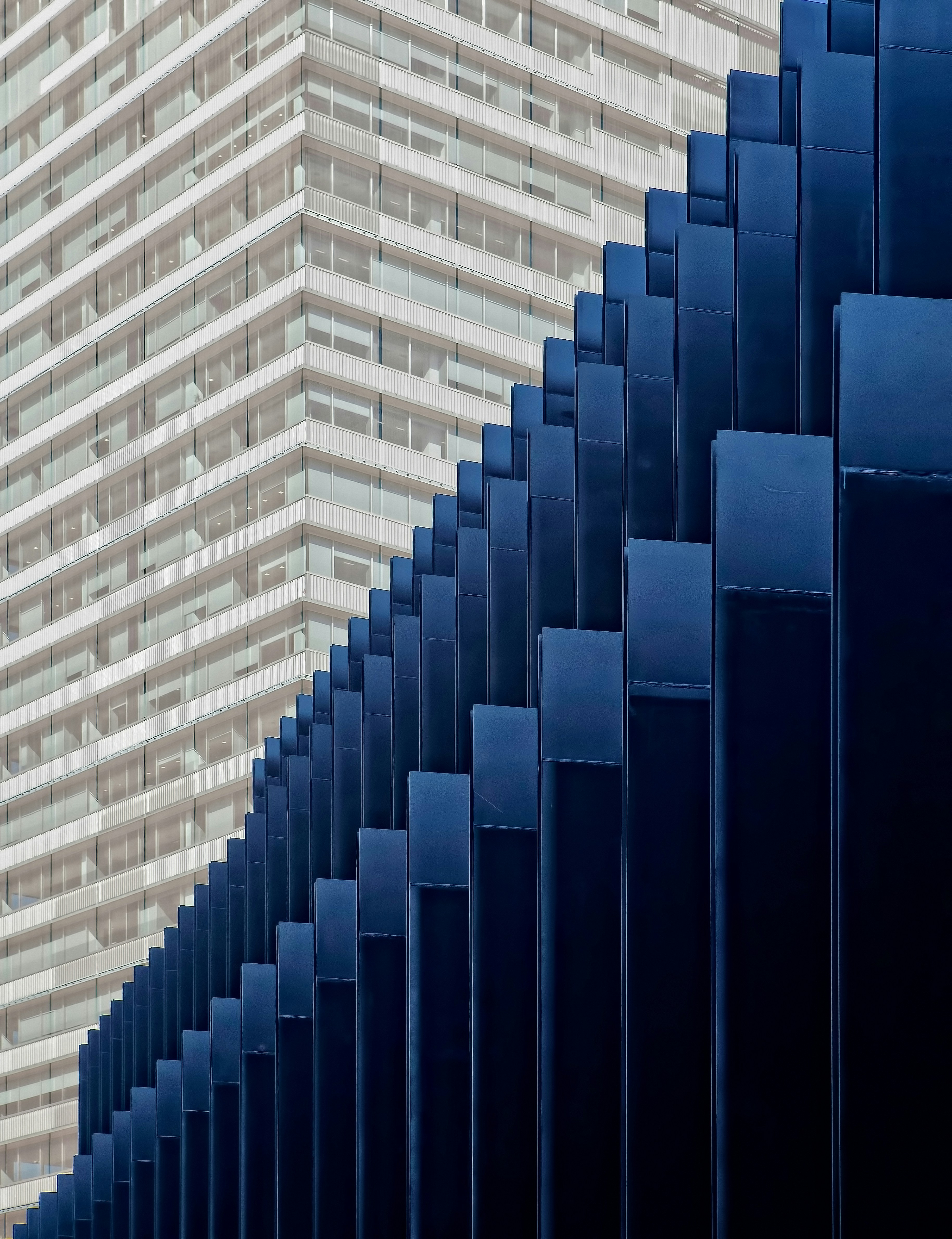 Abstract architectural composition featuring a series of blue, layered structures contrasted against a backdrop of a modern, white high-rise building.