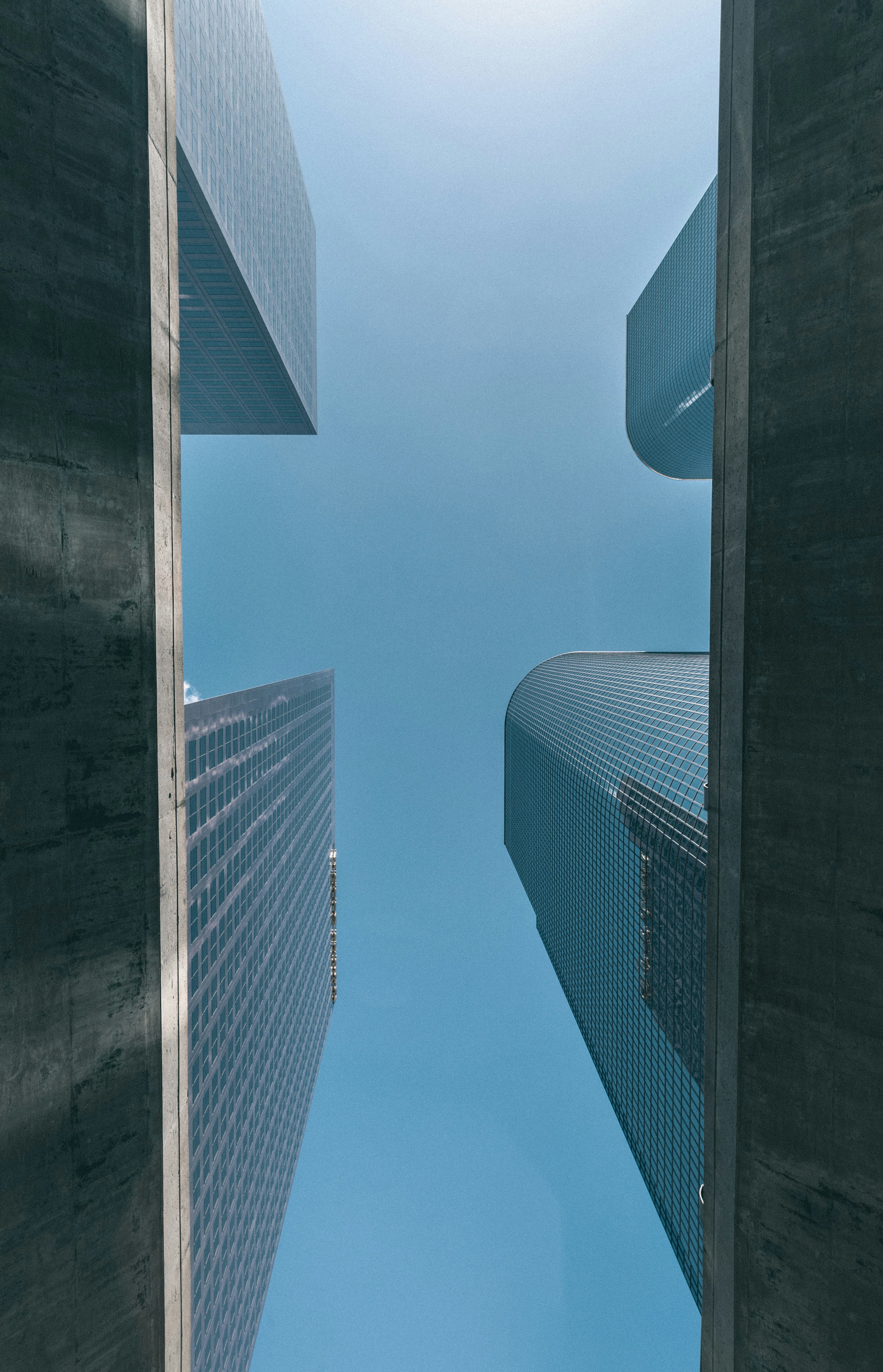 Looking up through a narrow gap between towering skyscrapers against a clear blue sky.