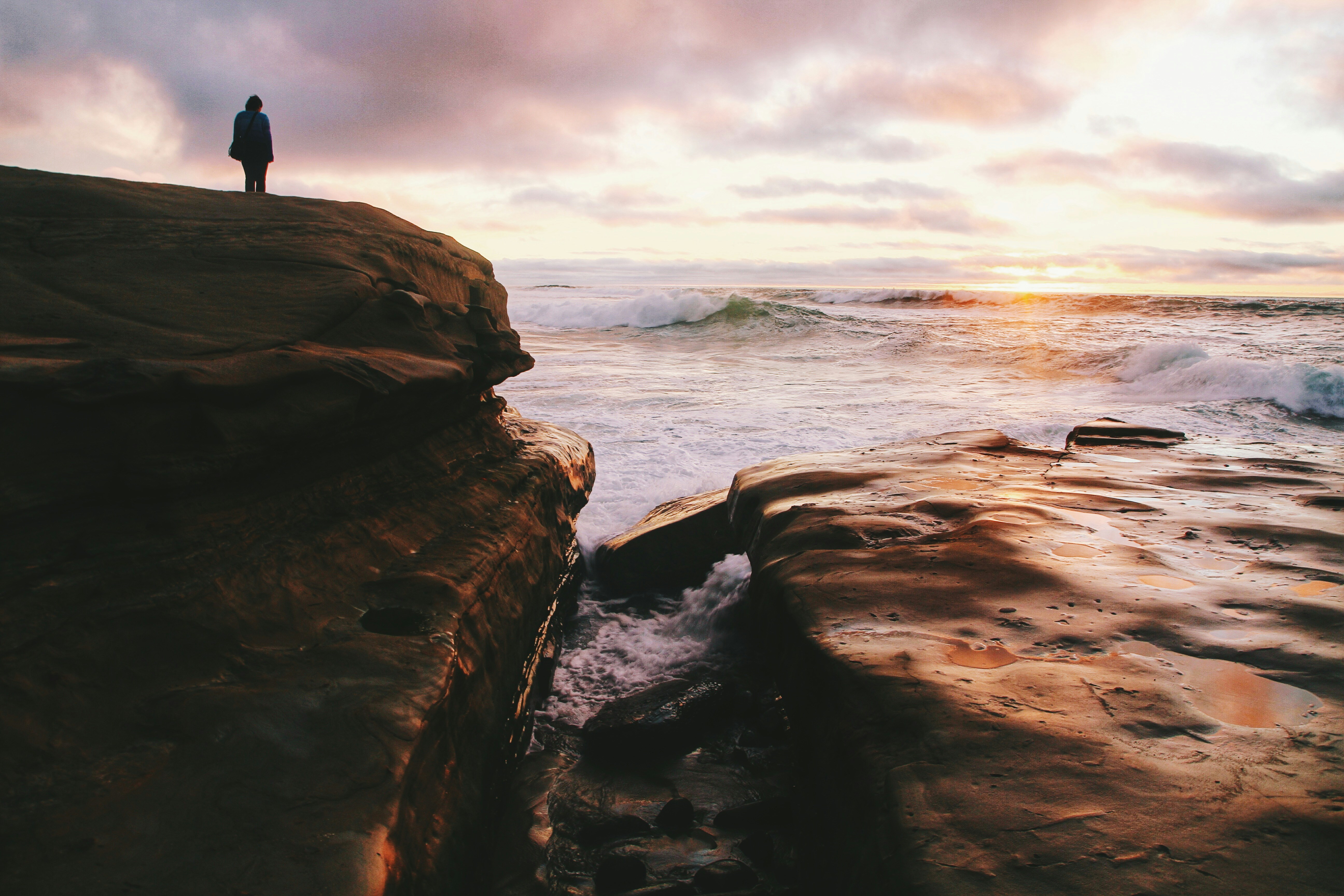Person standing on a cliff facing body of water photo – Free Coast ...