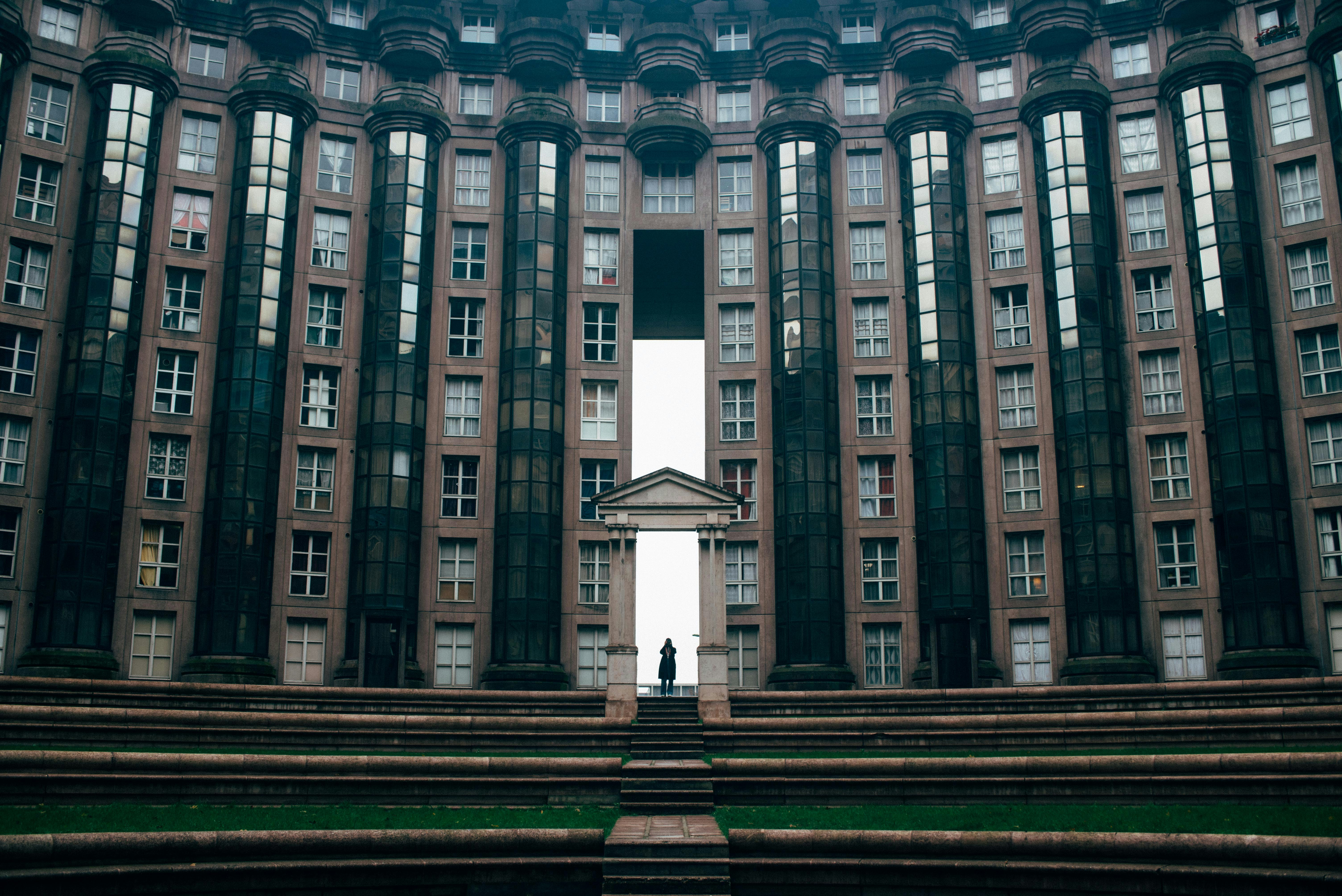 Tall, imposing columns of a monumental building frame a solitary figure standing at the entrance.
