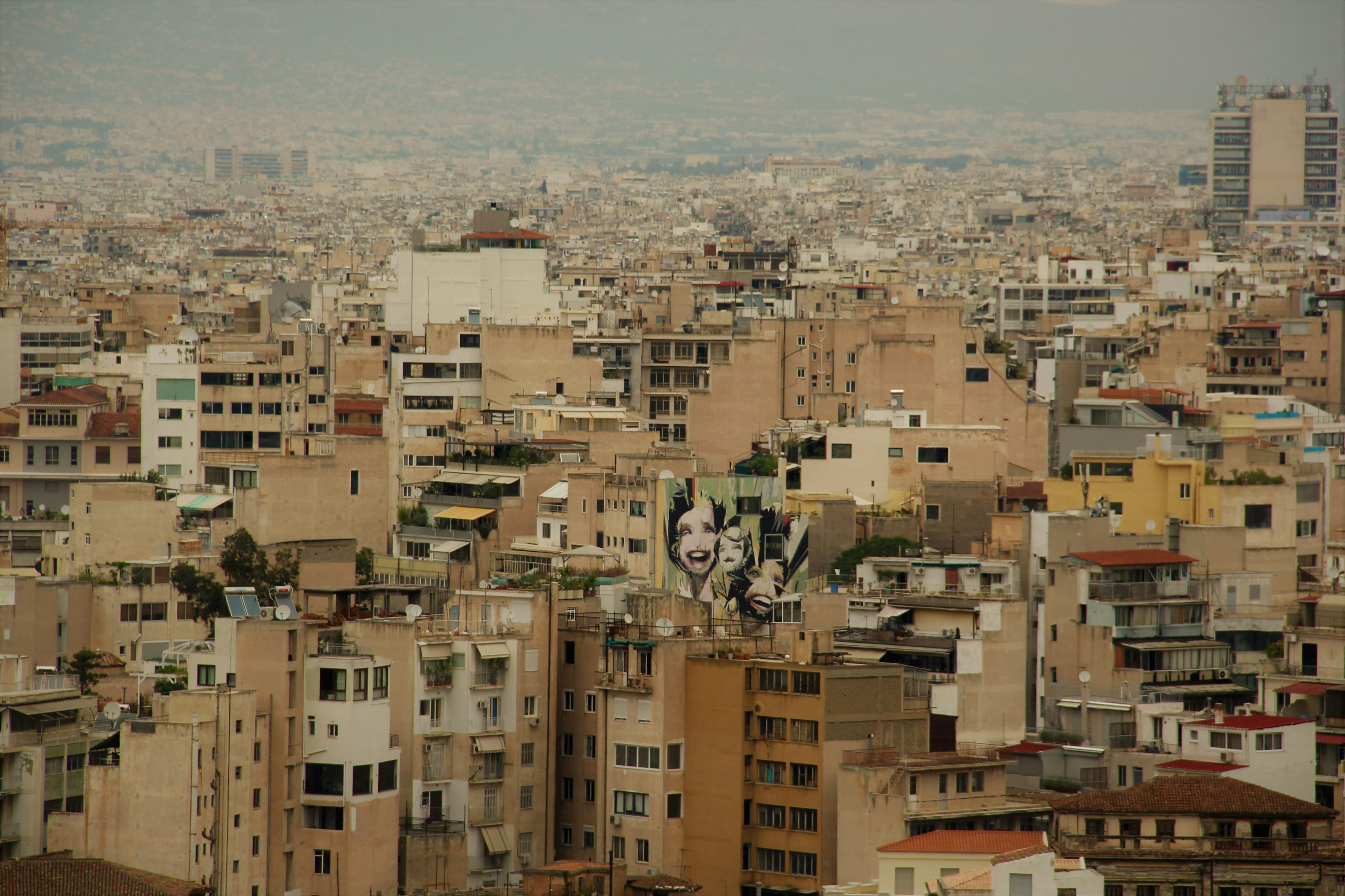 Dense cityscape of Athens with a multitude of beige and white buildings under a cloudy sky.