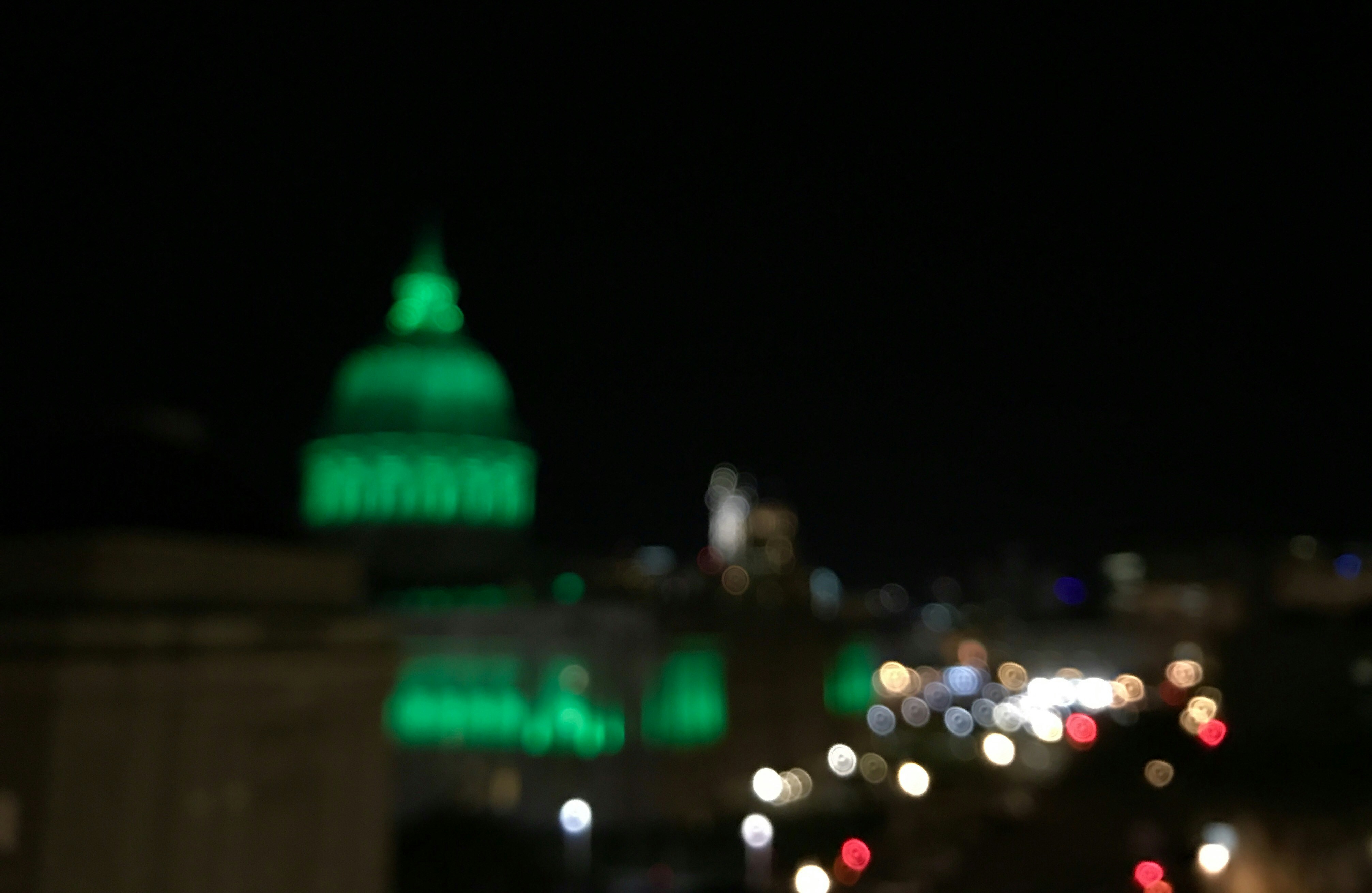Blurred view of the U.S. Capitol building illuminated in green against a dark night sky.