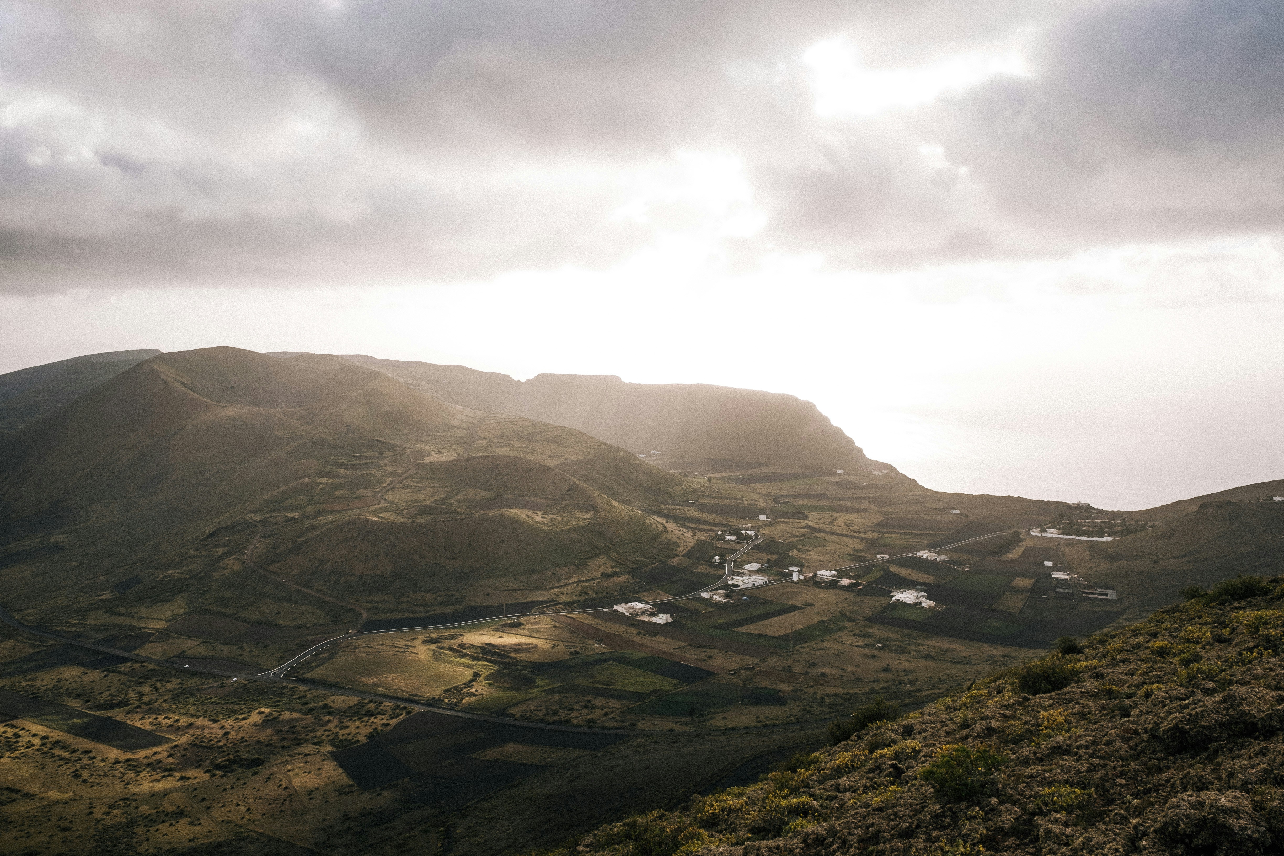 Sunlight breaks through clouds illuminating a rugged landscape with rolling hills and scattered settlements.
