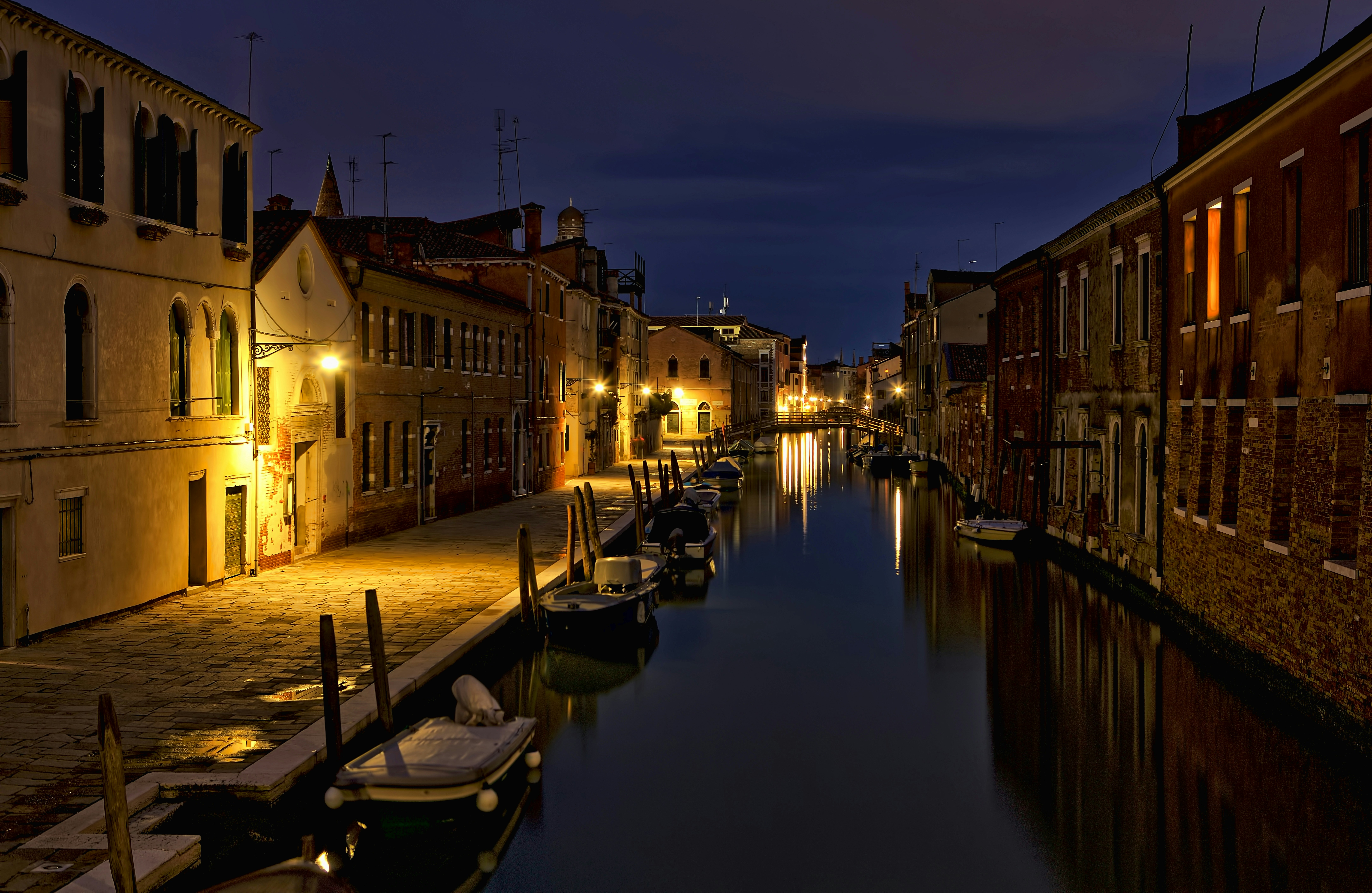 Serene canal scene in Venice illuminated by warm streetlights, reflecting on the water's surface.