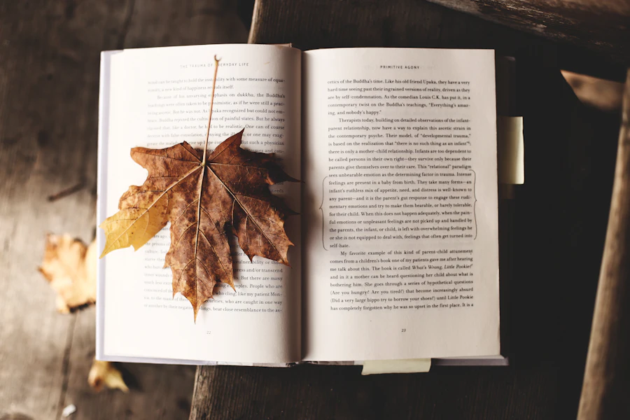 A dried maple leaf lies across the left page of an open book on a dark wooden table. Warm natural light creates a cozy, seasonal still life.