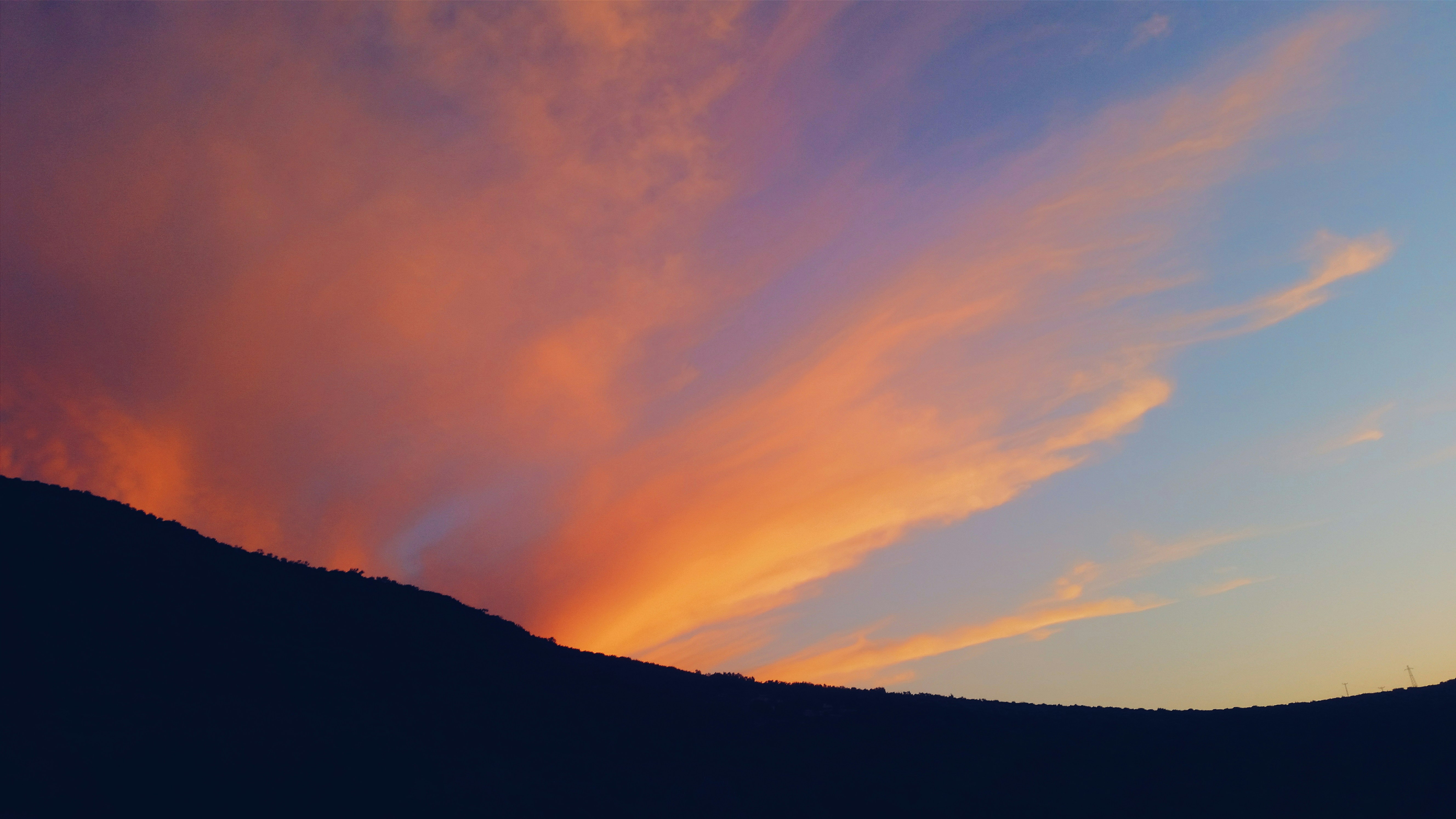 Vibrant orange and pink clouds stretch across the sky at sunset, silhouetting a dark hillside.