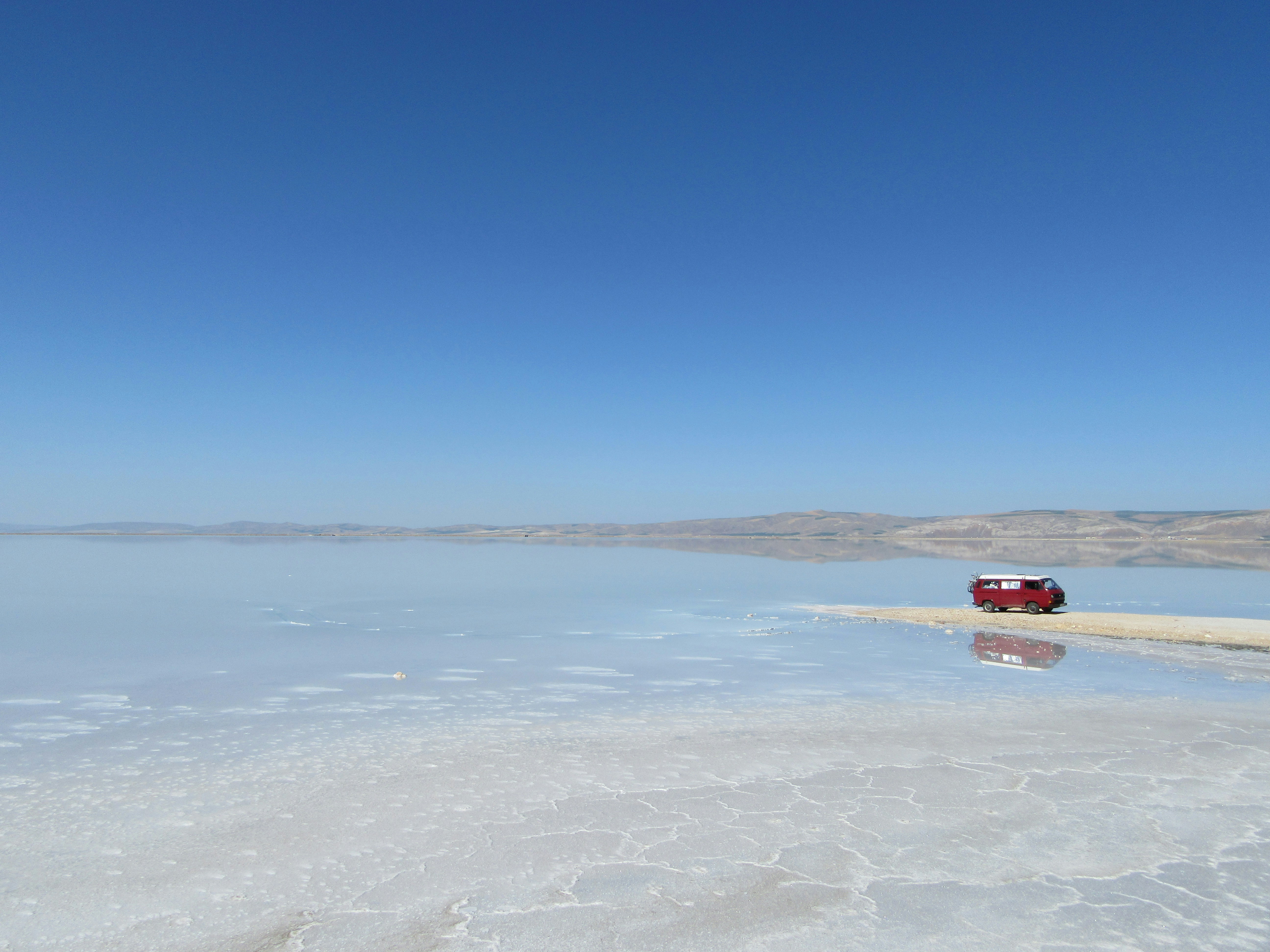 A vibrant red van parked on the glistening salt flats under a clear blue sky, showcasing the serene landscape and vastness of the area.