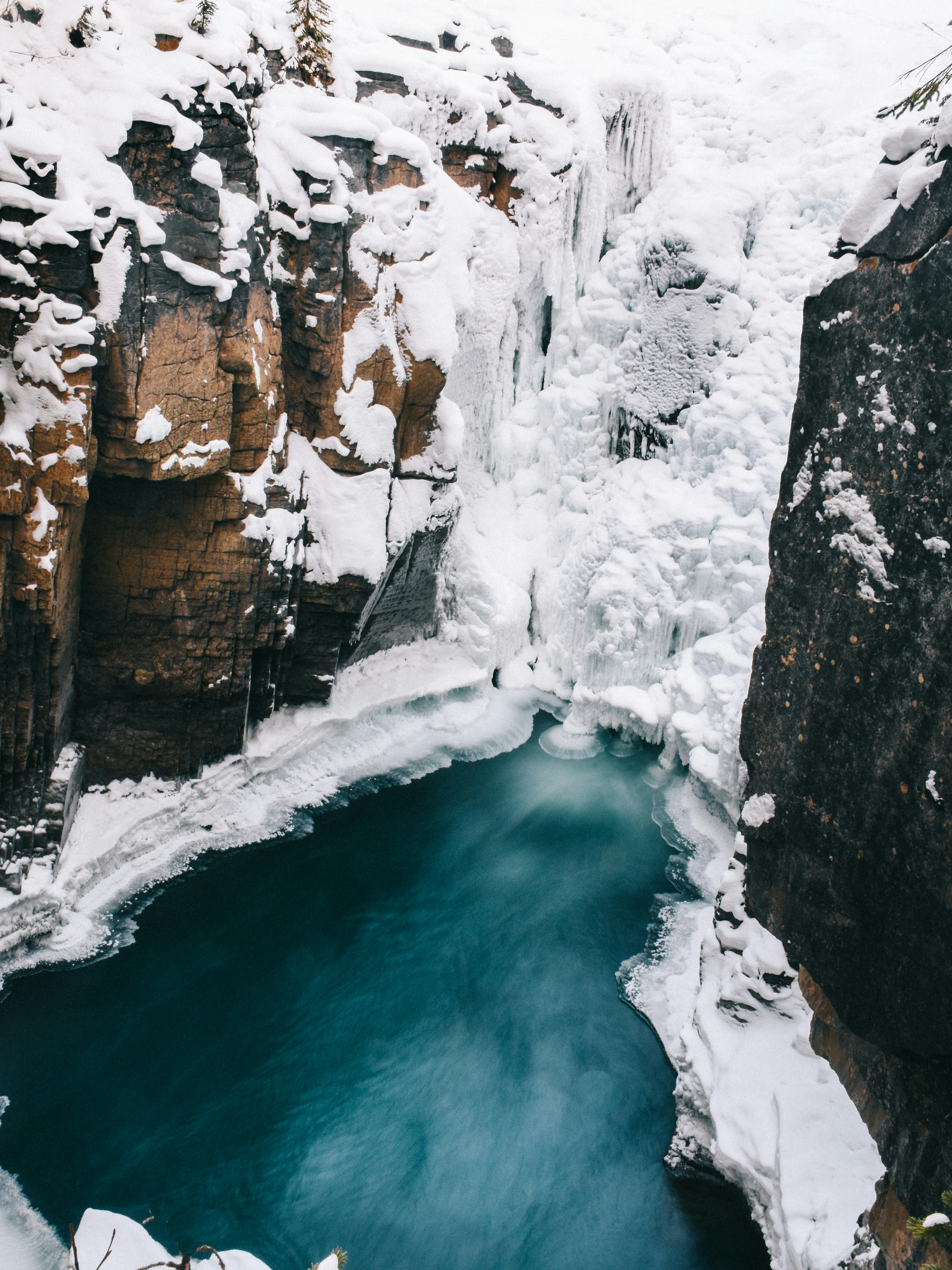 Majestic frozen waterfall cascading into a turquoise pool, surrounded by snow-covered cliffs. The scene captures the serene beauty of winter's embrace.