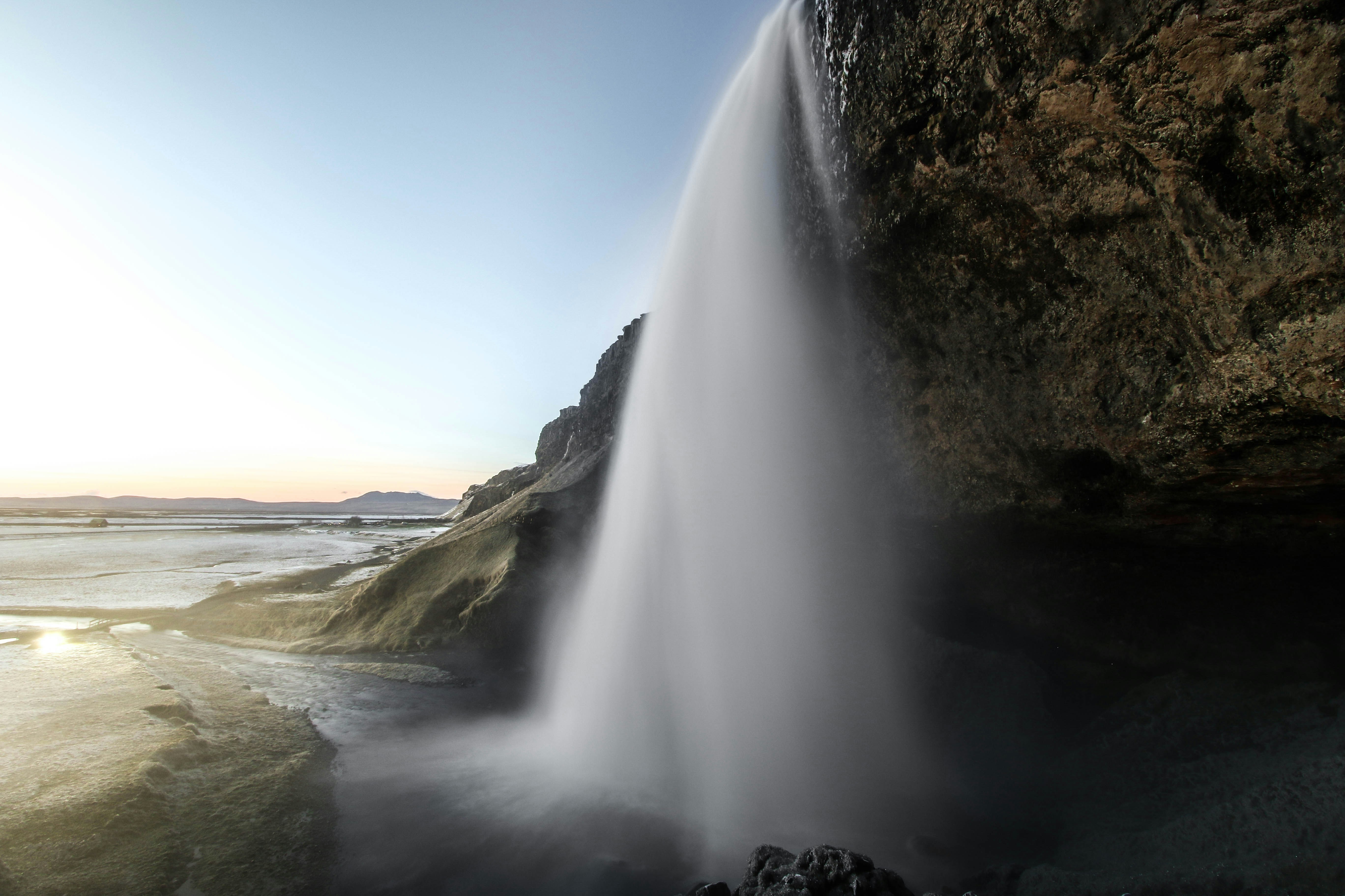 Waterfall cascading down rocky cliffs, surrounded by a serene landscape at dusk.
