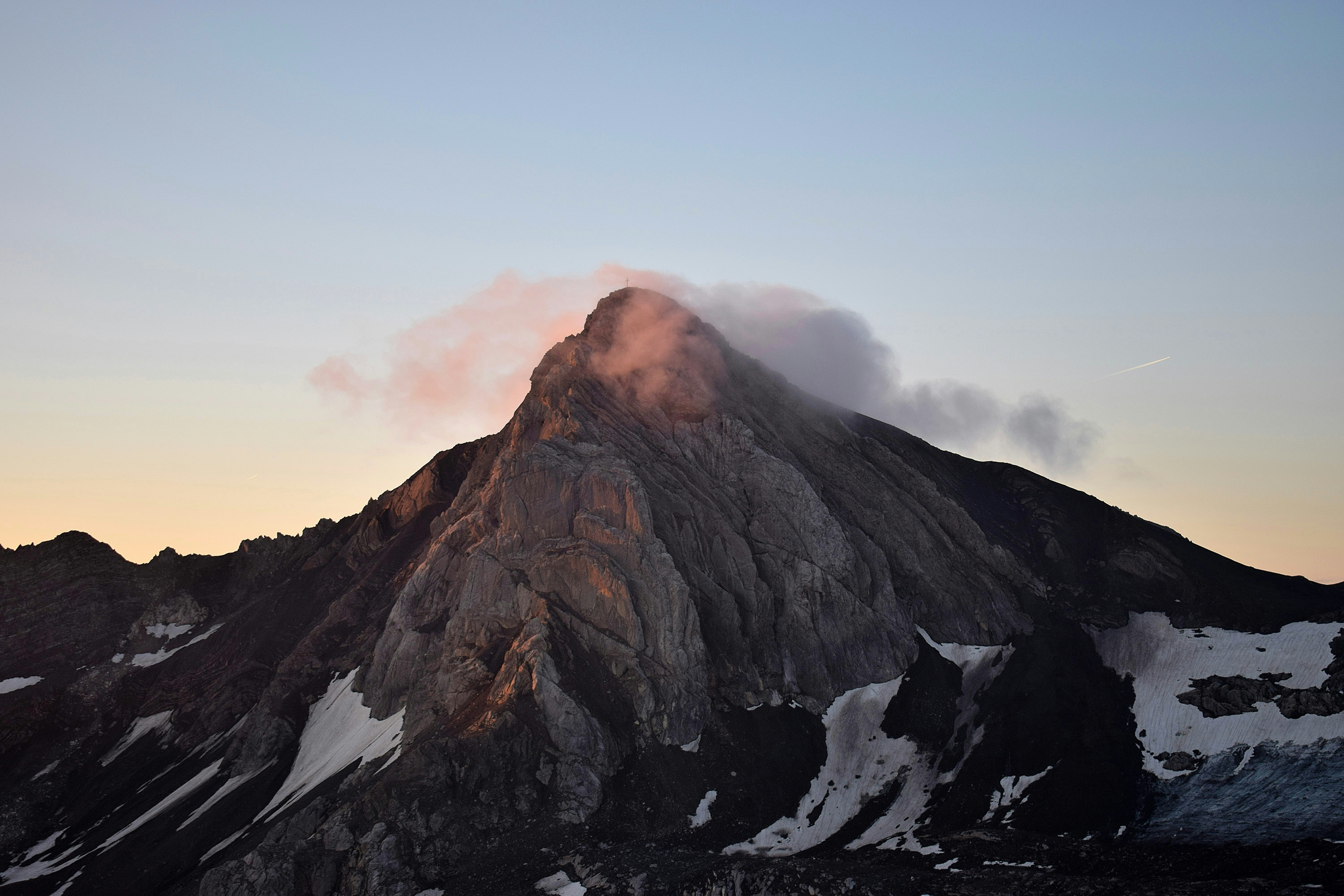 Majestic mountain peak with a soft cloud shrouding its summit at sunset.