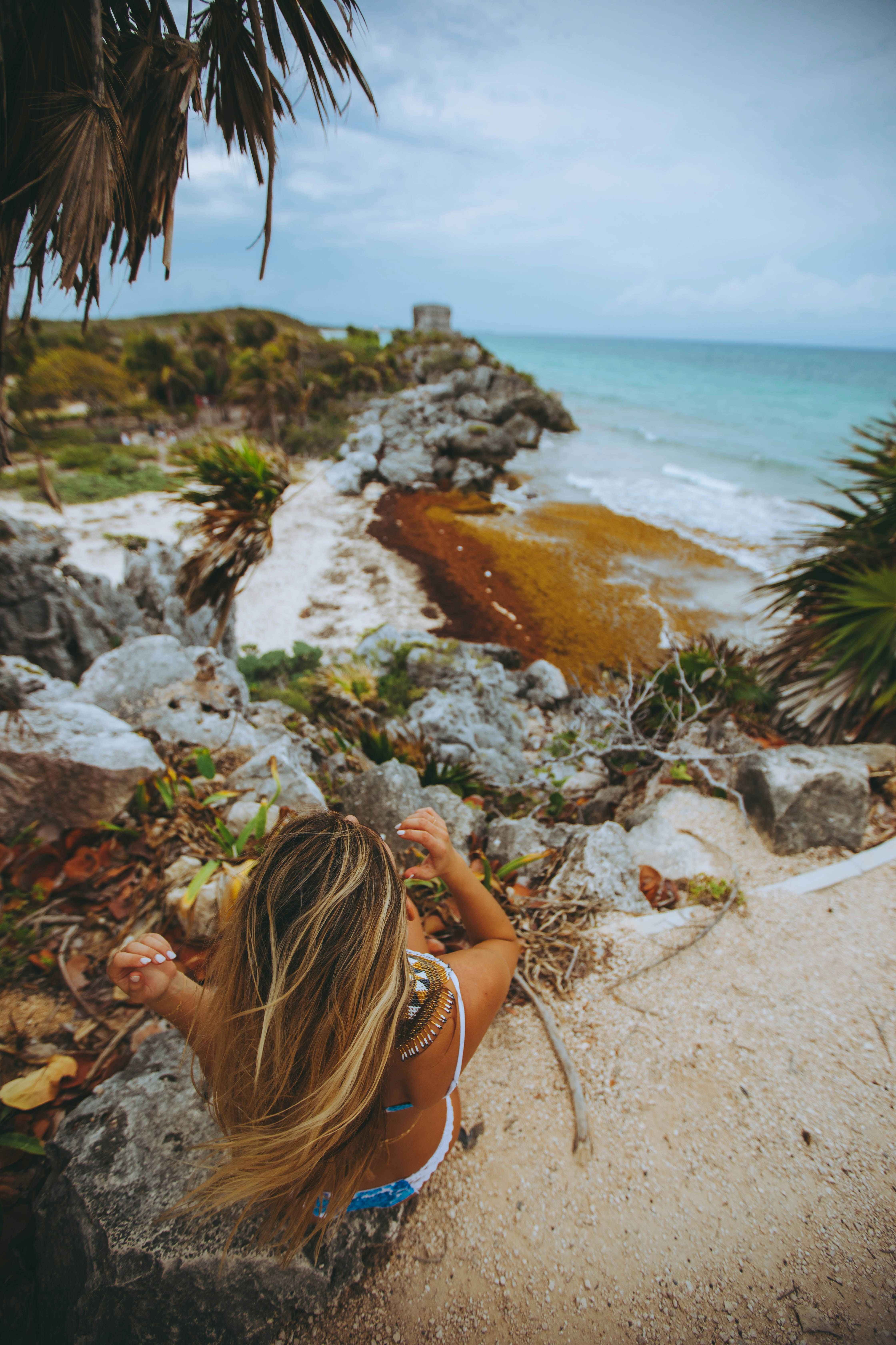 Sea-salt Quiet: A girl perched on sunlit rocks overlooking a turquoise coast.
